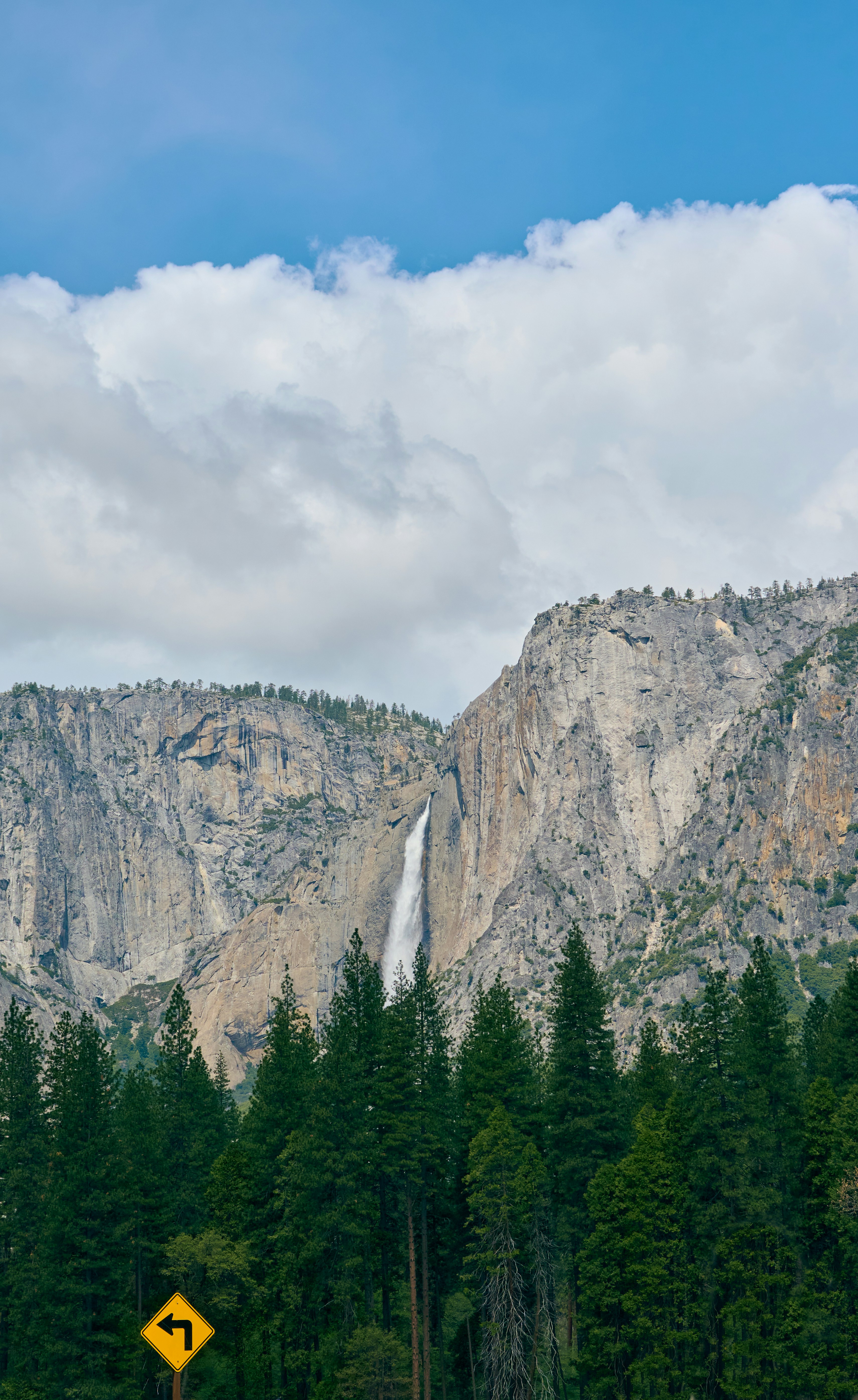 A waterfall cascades down rocky mountains with green trees.