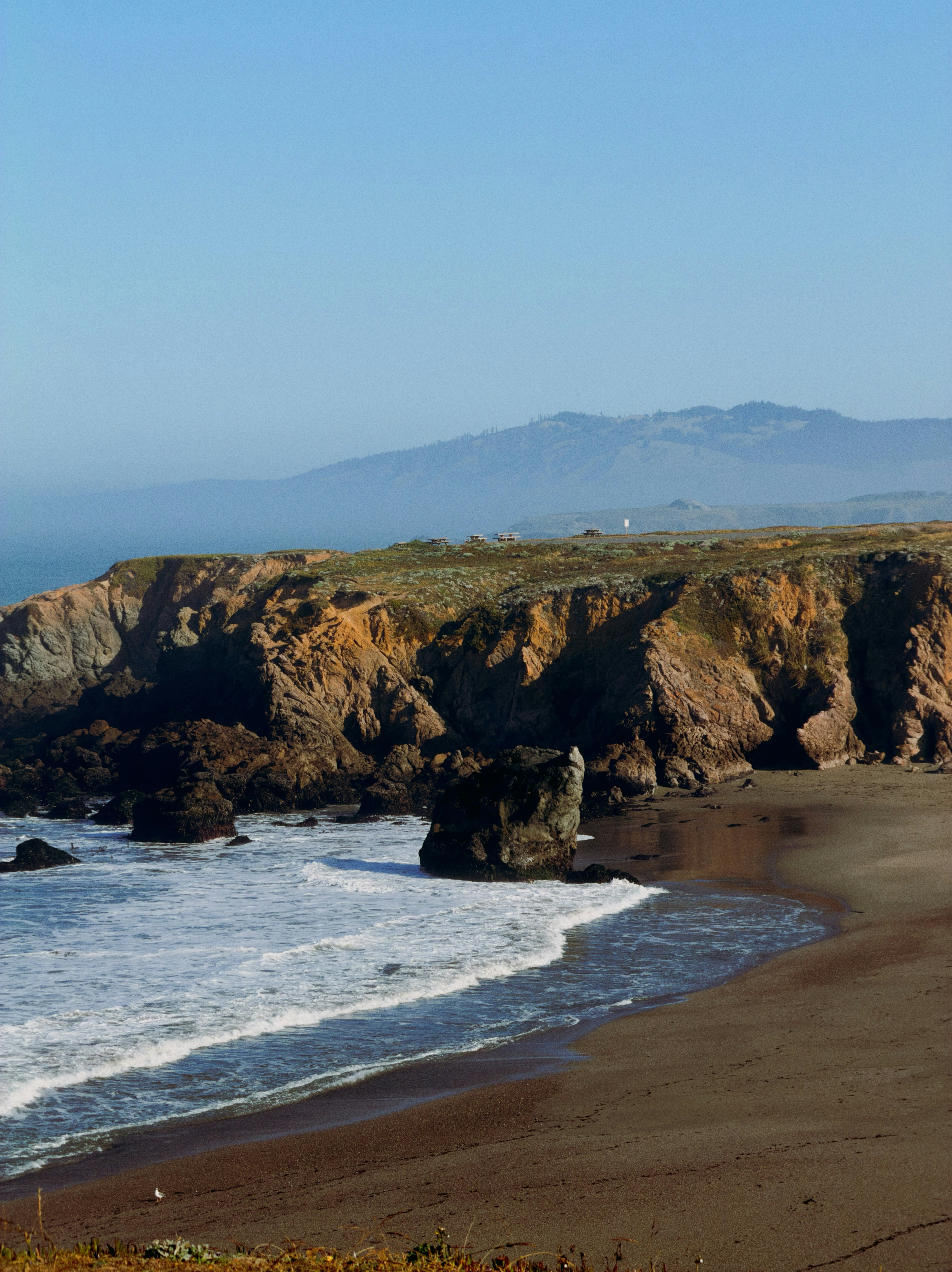 Coastal Cliffscape at Dusk: Waves, Rock, and Far Mountains