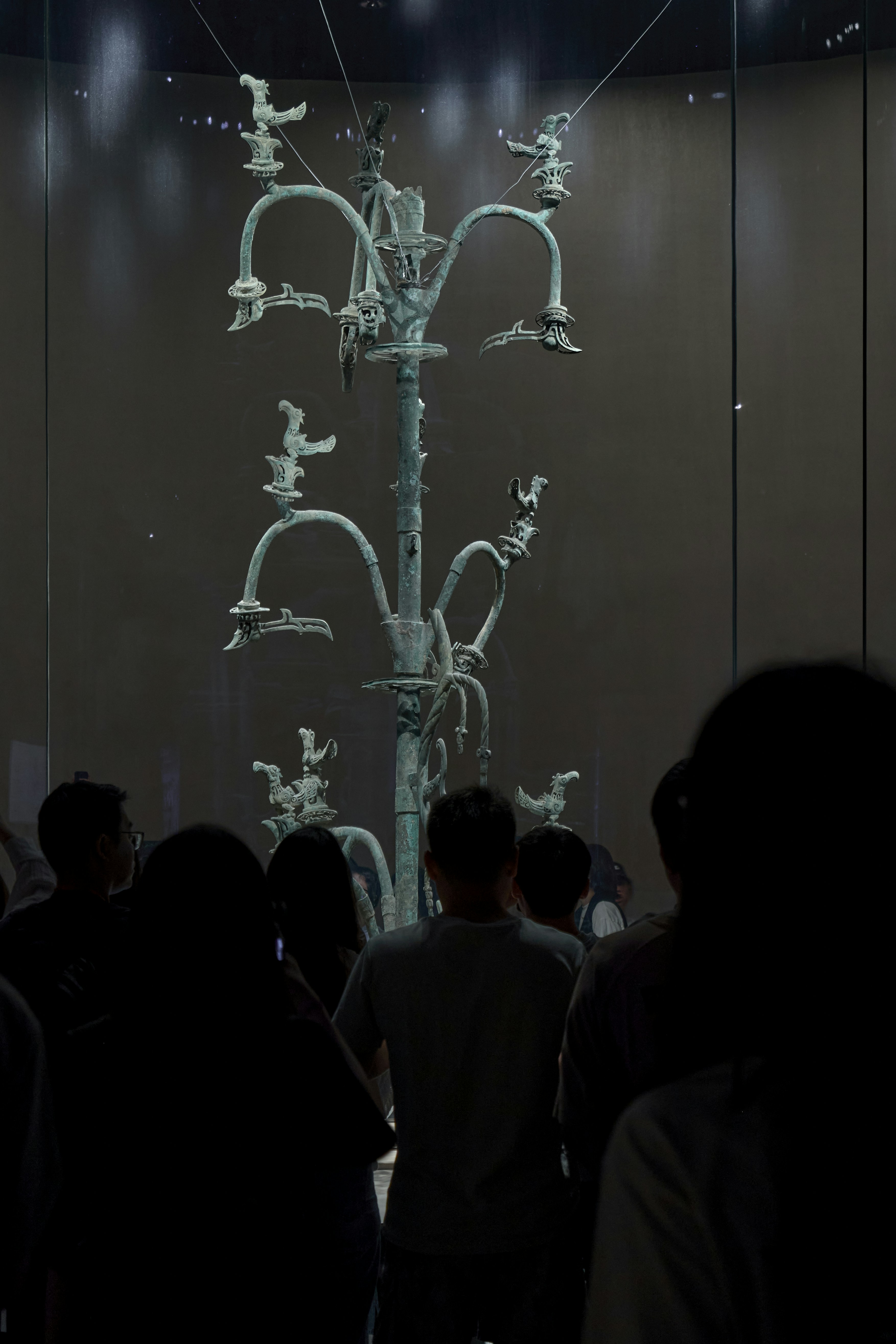 Silhouettes of people viewing an ancient bronze tree sculpture.