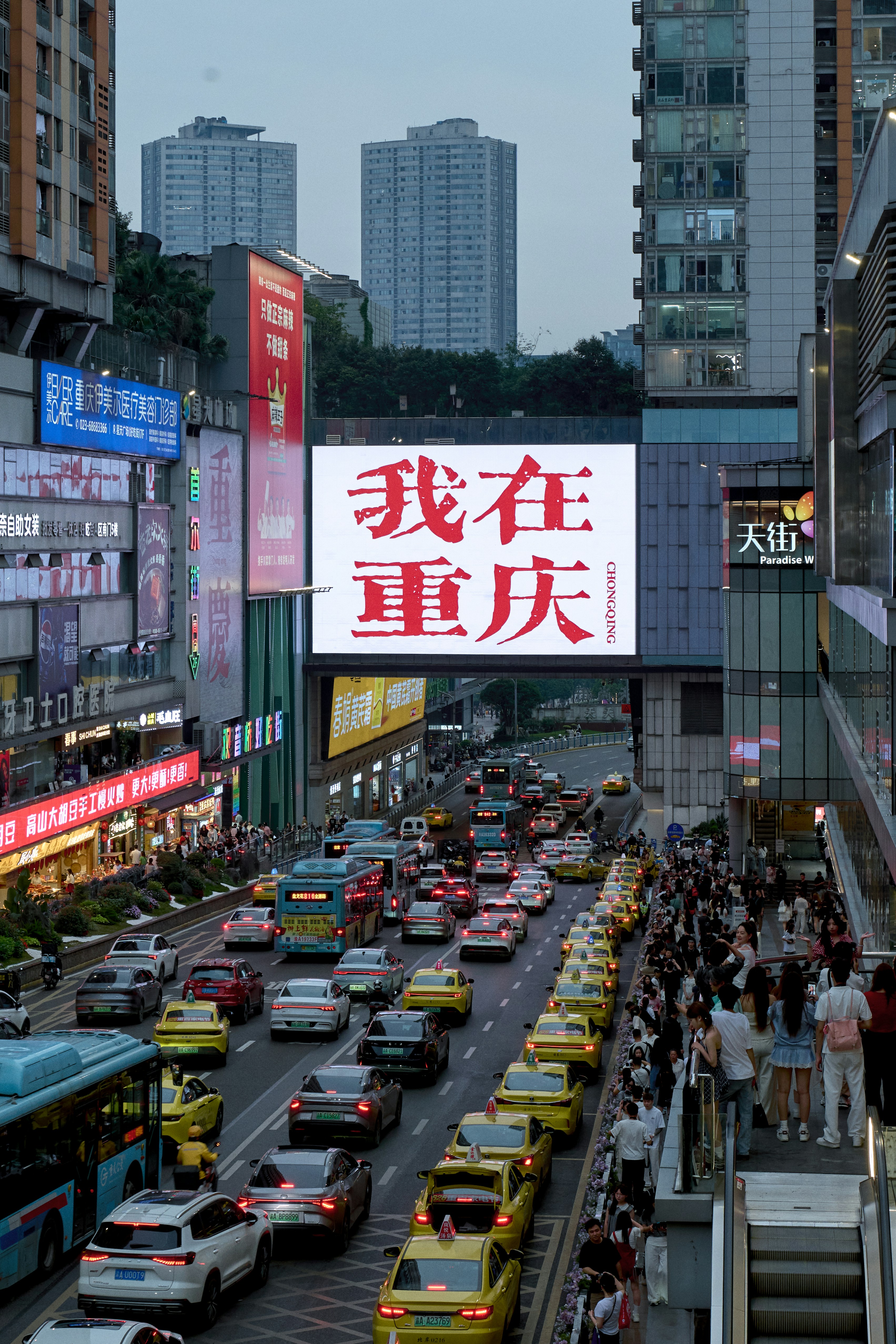 Busy city street with traffic, pedestrians, and chinese illuminated sign.