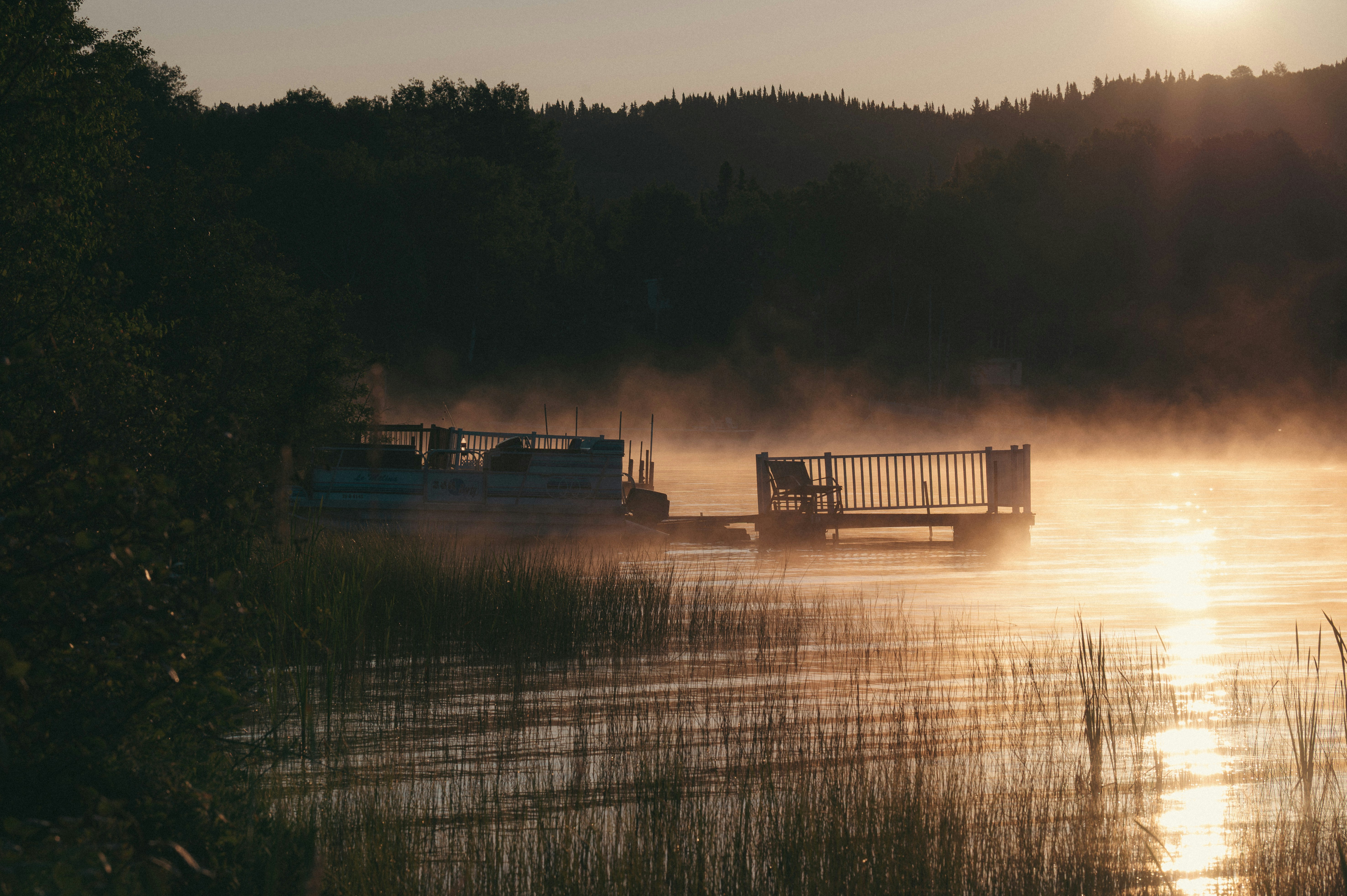 A misty lake at sunrise with a dock and boat.