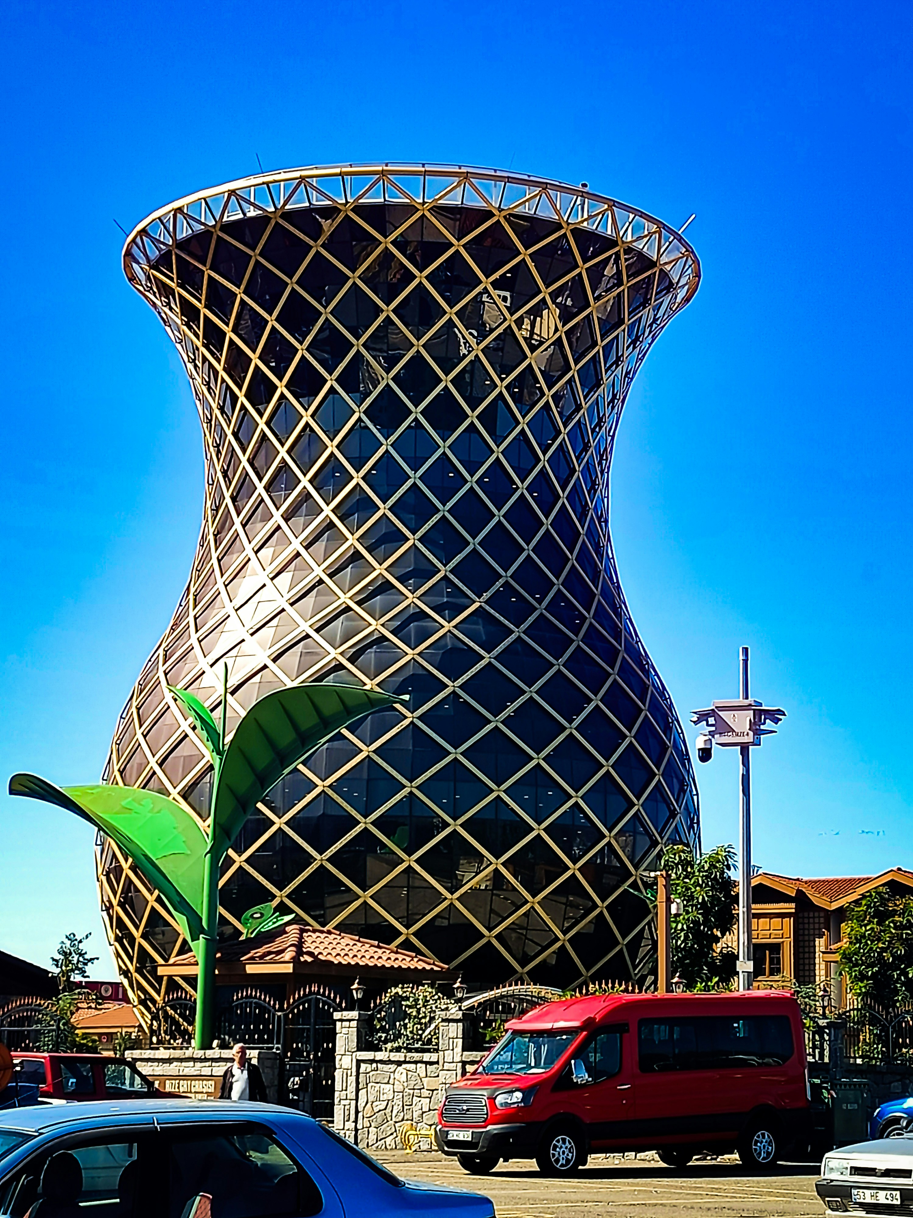 Unique vase-shaped building with leaf sculpture under blue sky.