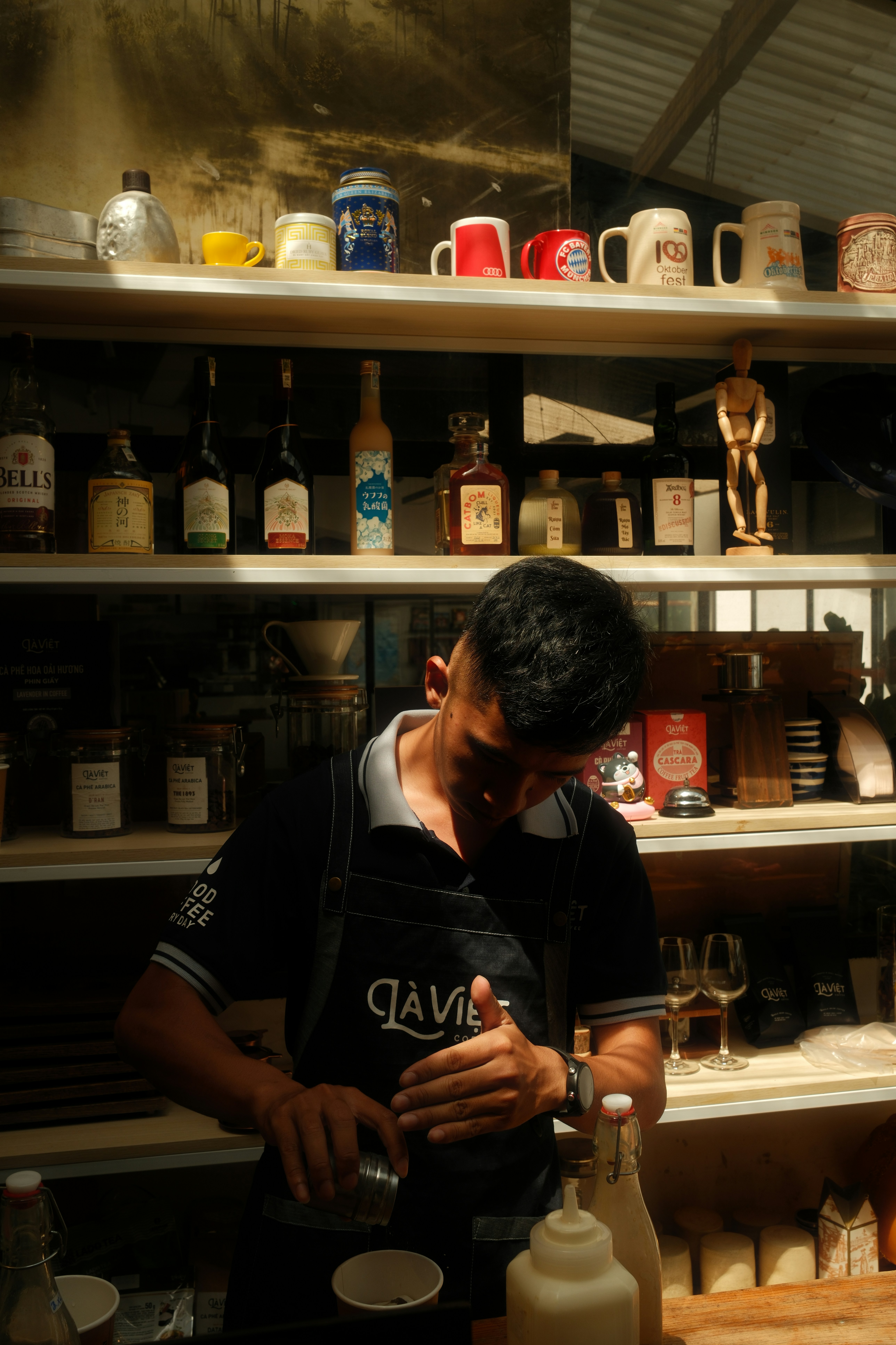 Barista at dusk: pouring precision beneath rows of bottles