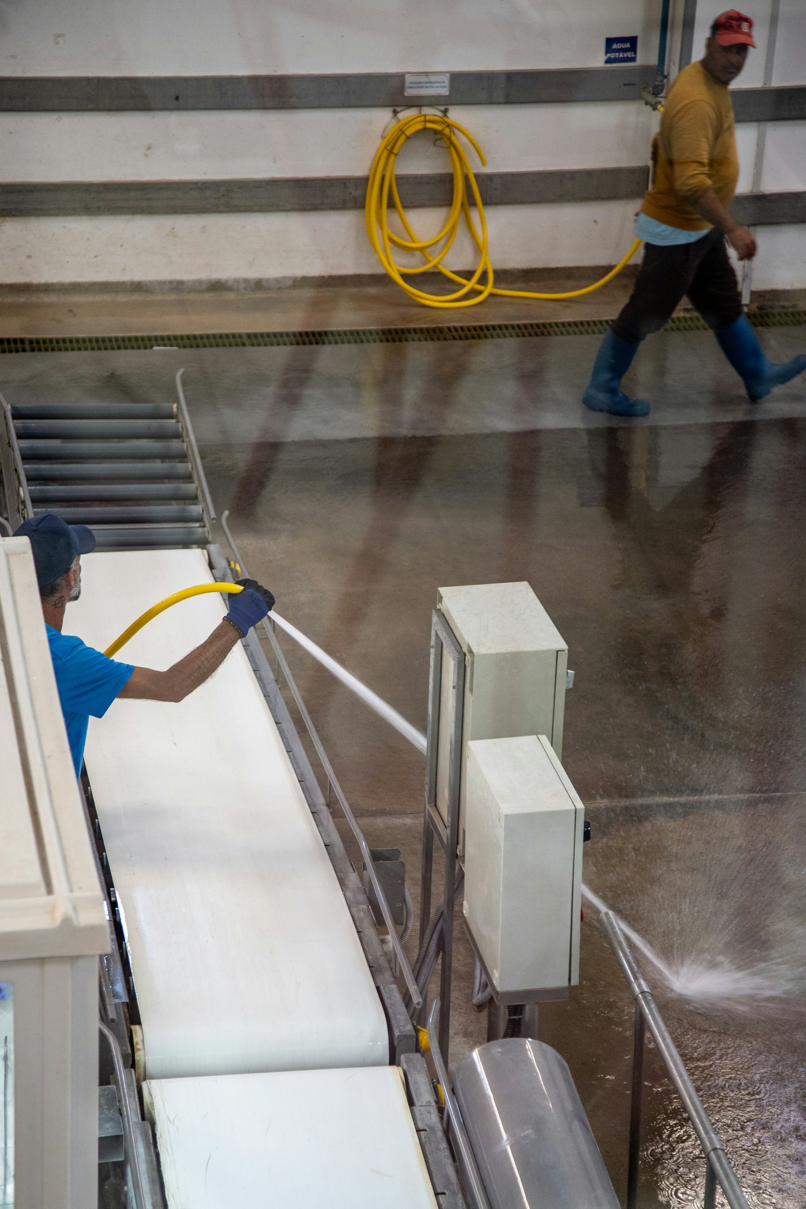 Hose at the Ready: A Gloved Worker Reaches Over a Conveyor