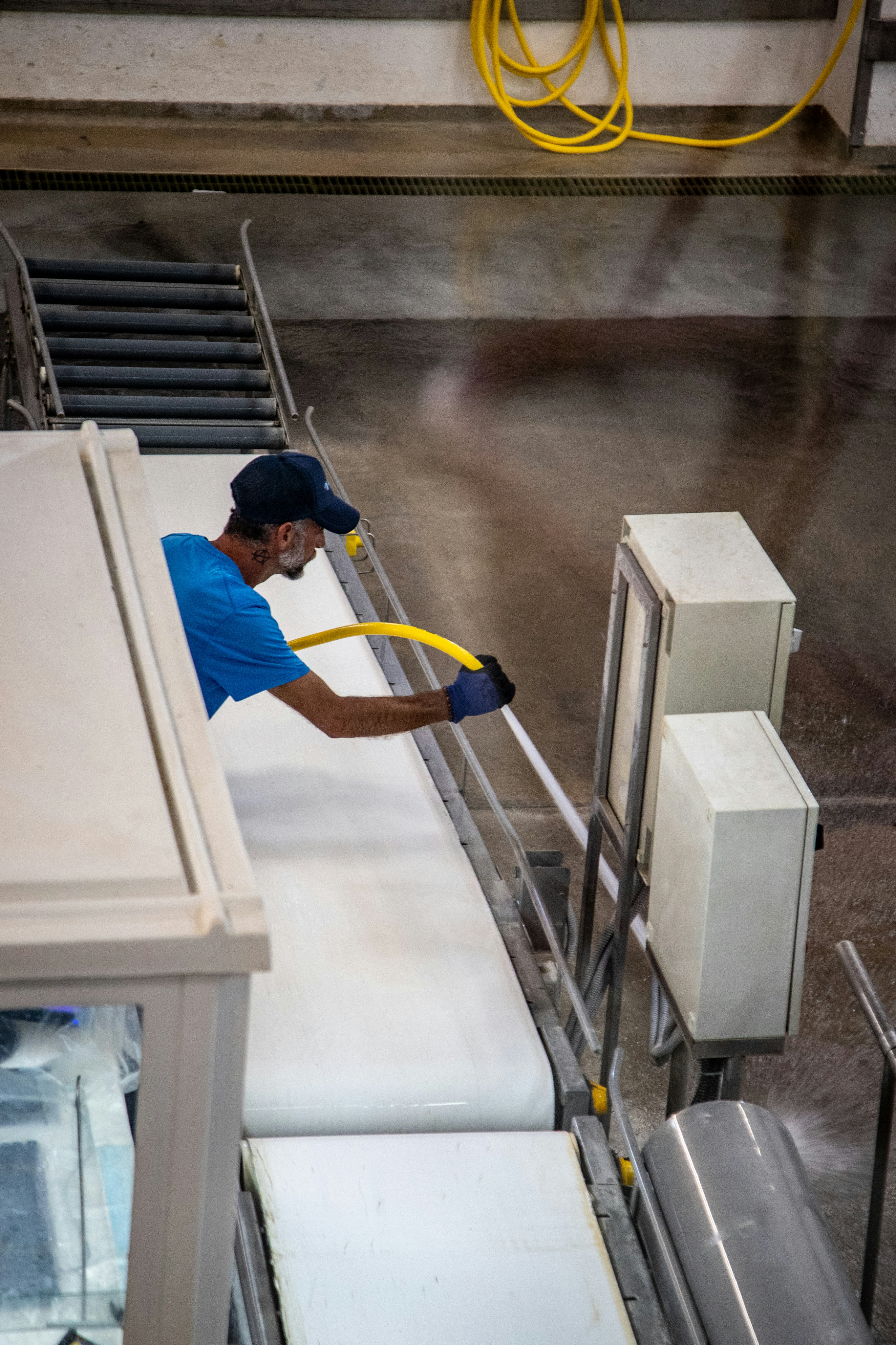 Operator in blue shirt guiding a high-pressure hose along a conveyor