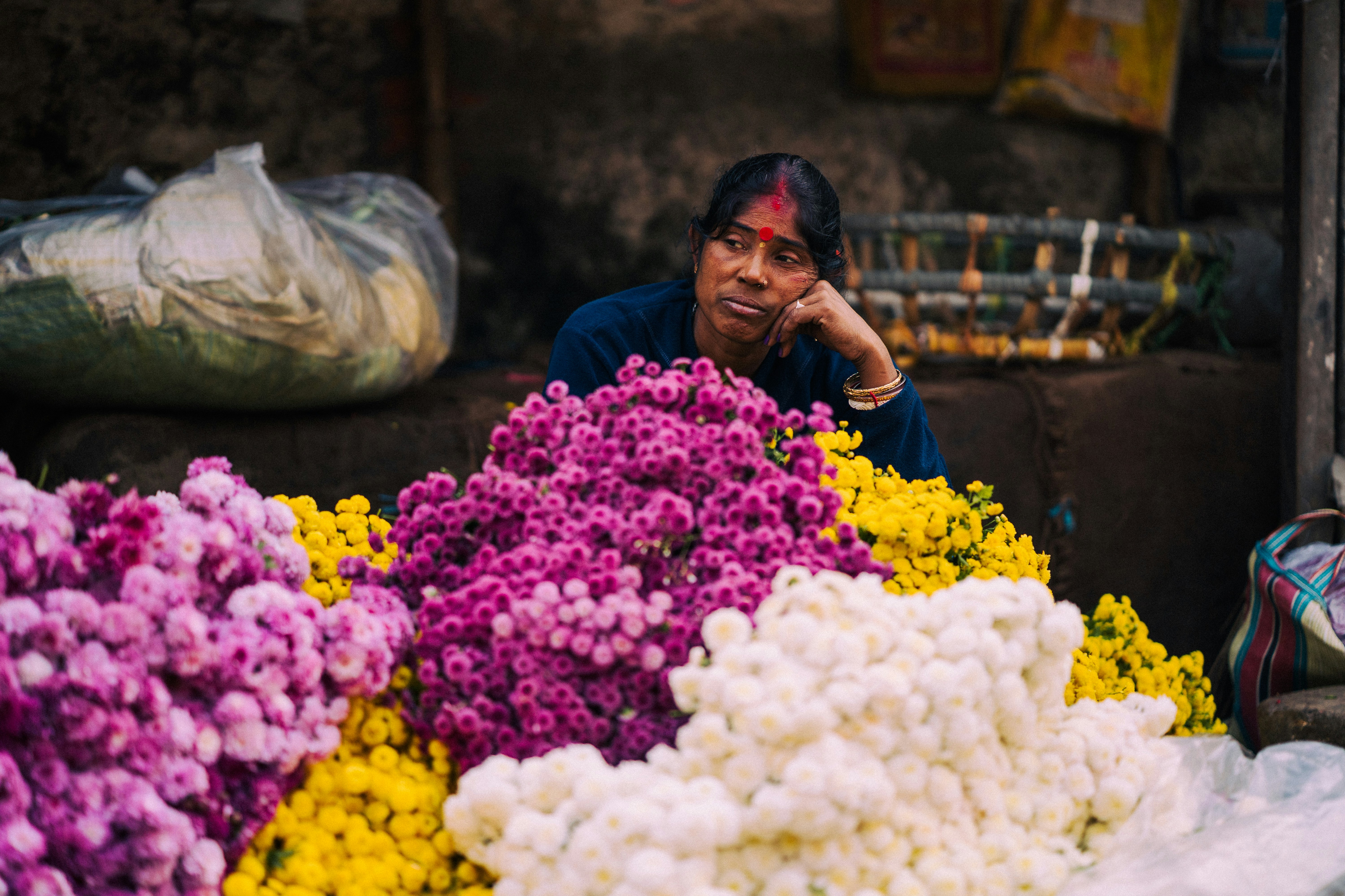 A woman sits behind a vibrant display of colorful flowers.