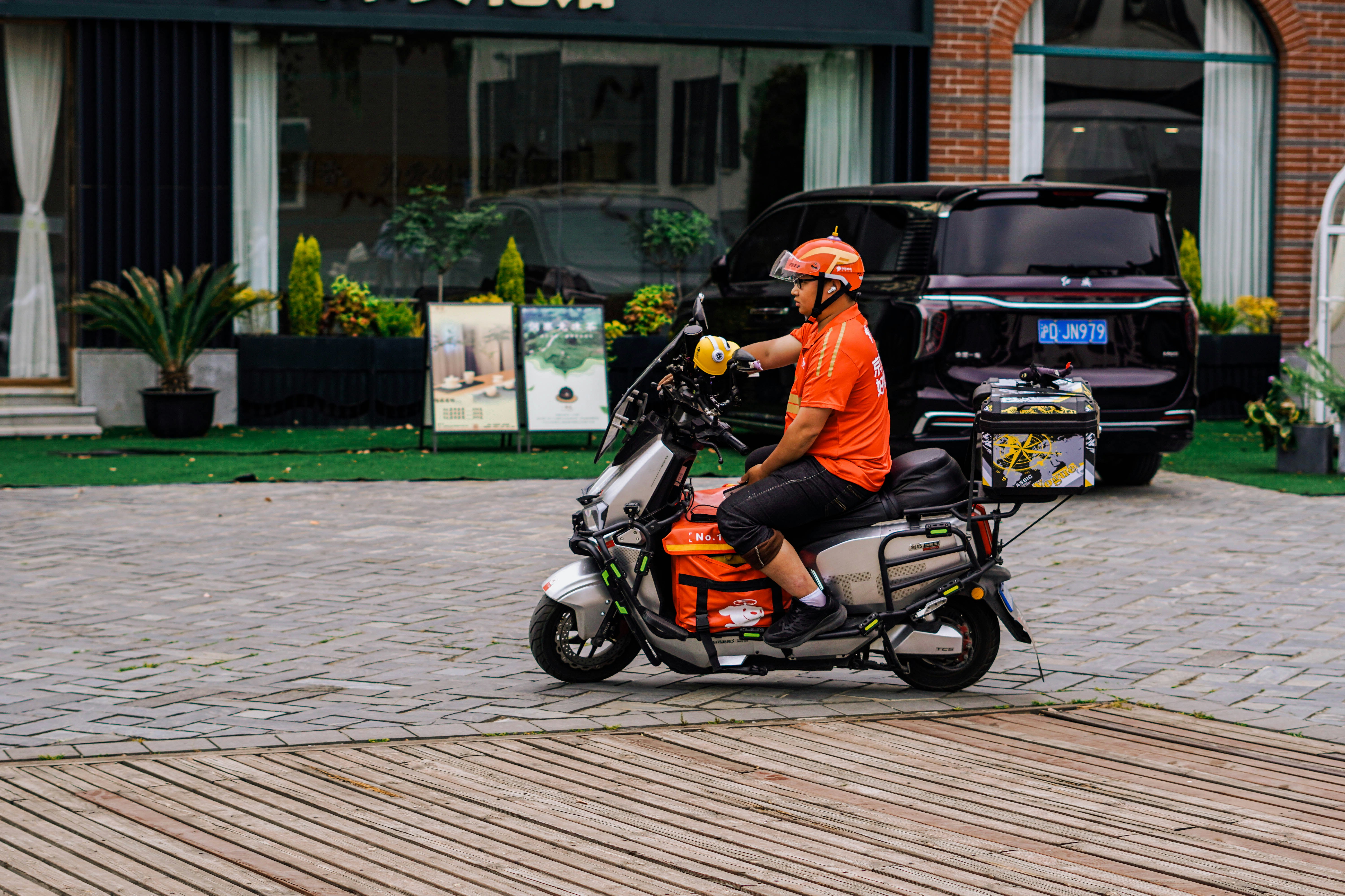 Orange-clad courier on a city scooter glides past a stylish storefront