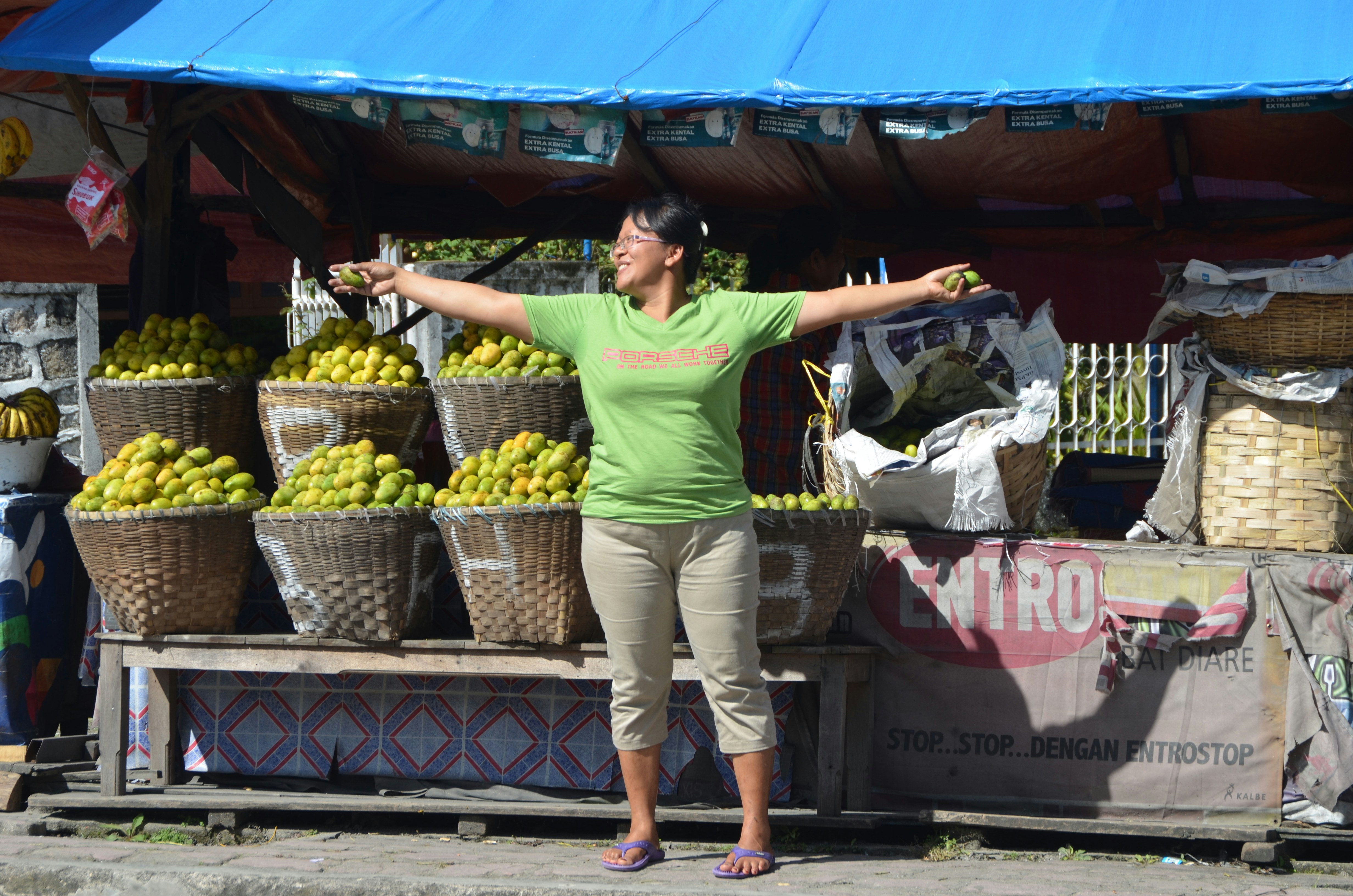Arms Wide to the Market: A Woman Balances Fruits Under a Blue Canopy