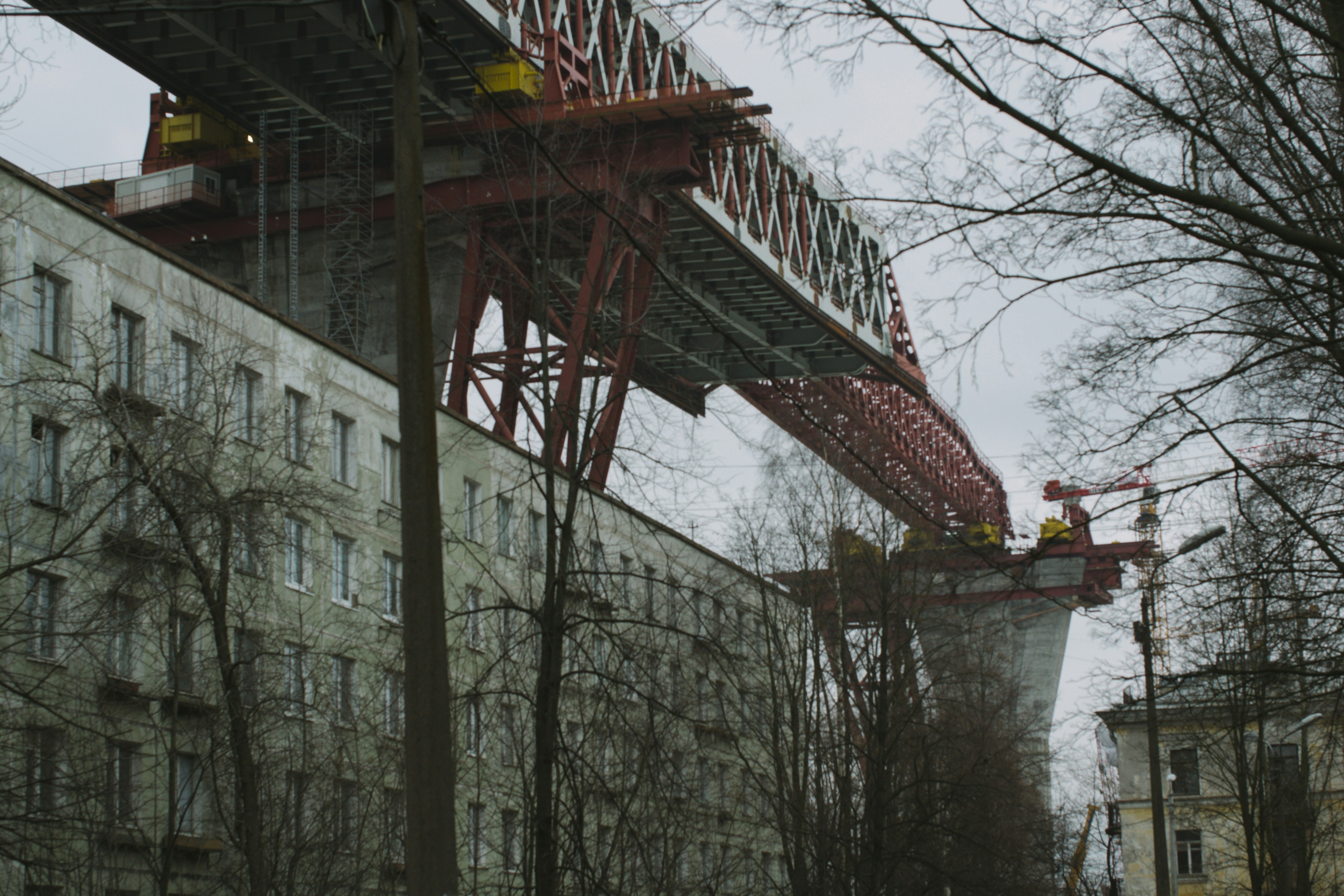 Under the Red Arch: A Partially Wrapped Bridge Looms Over a Quiet City