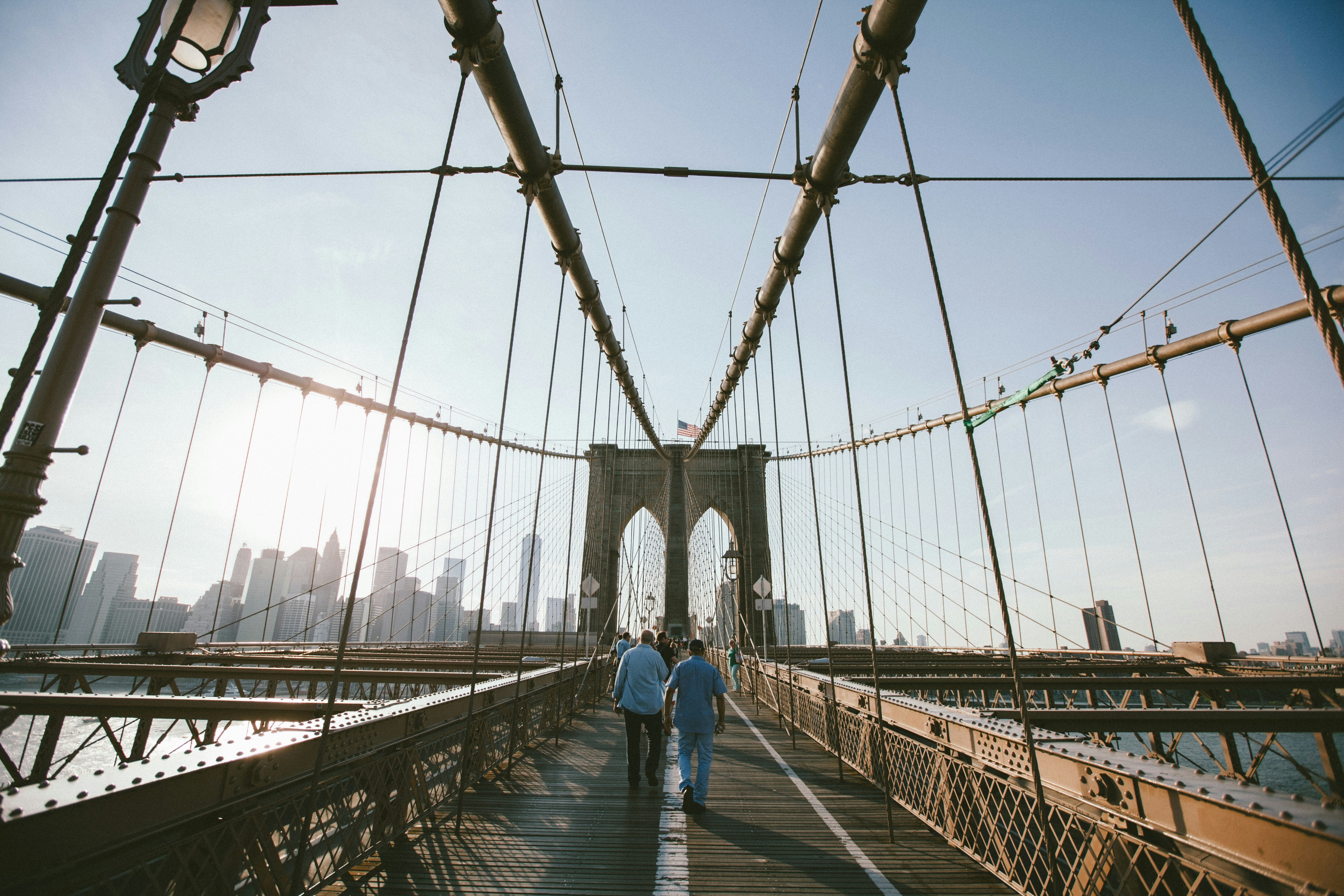 Two pedestrians stride toward the towers of a sunlit bridge at dawn