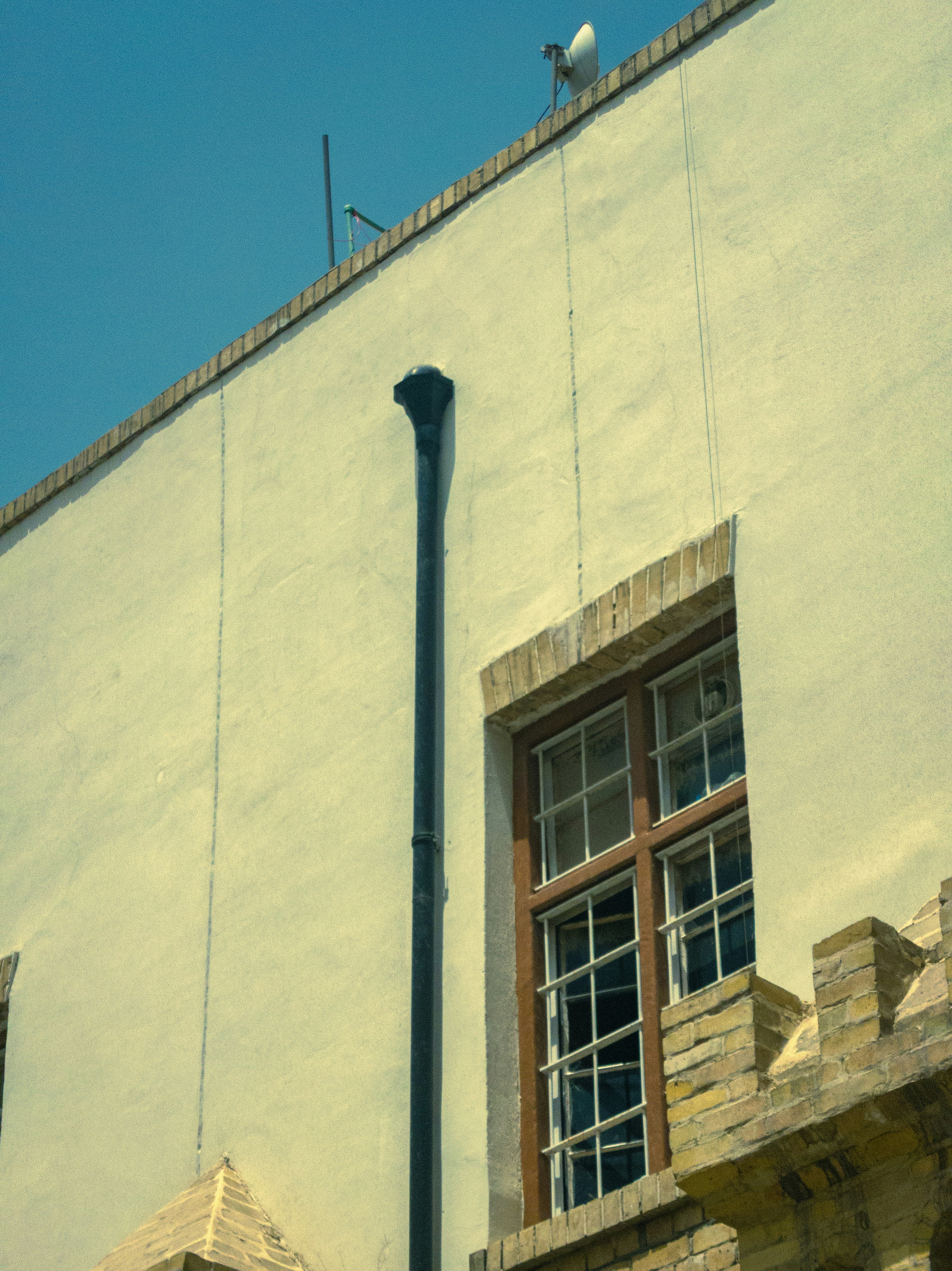 Vertical Pipe Against a Sunlit Facade