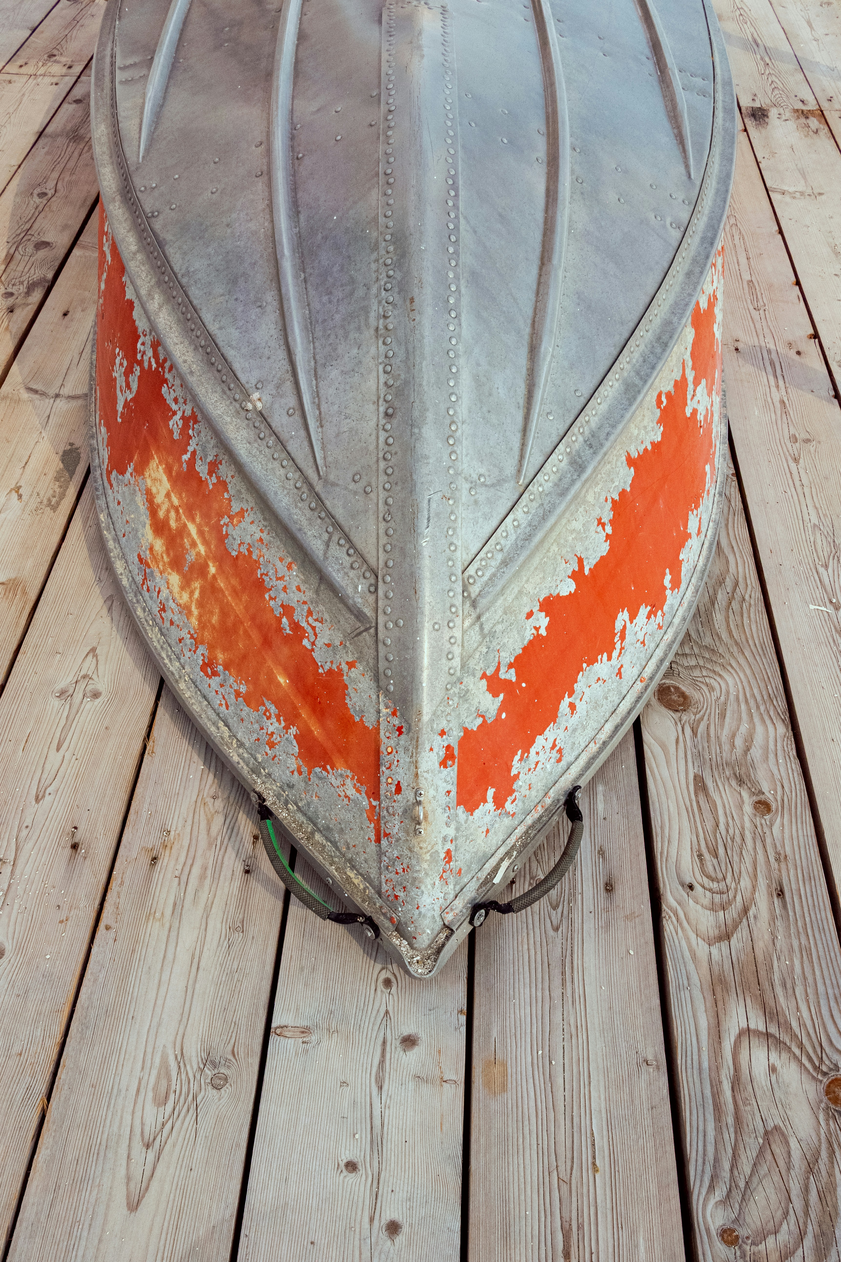 Weathered bow of a wooden docked vessel: orange flaked paint over riveted metal