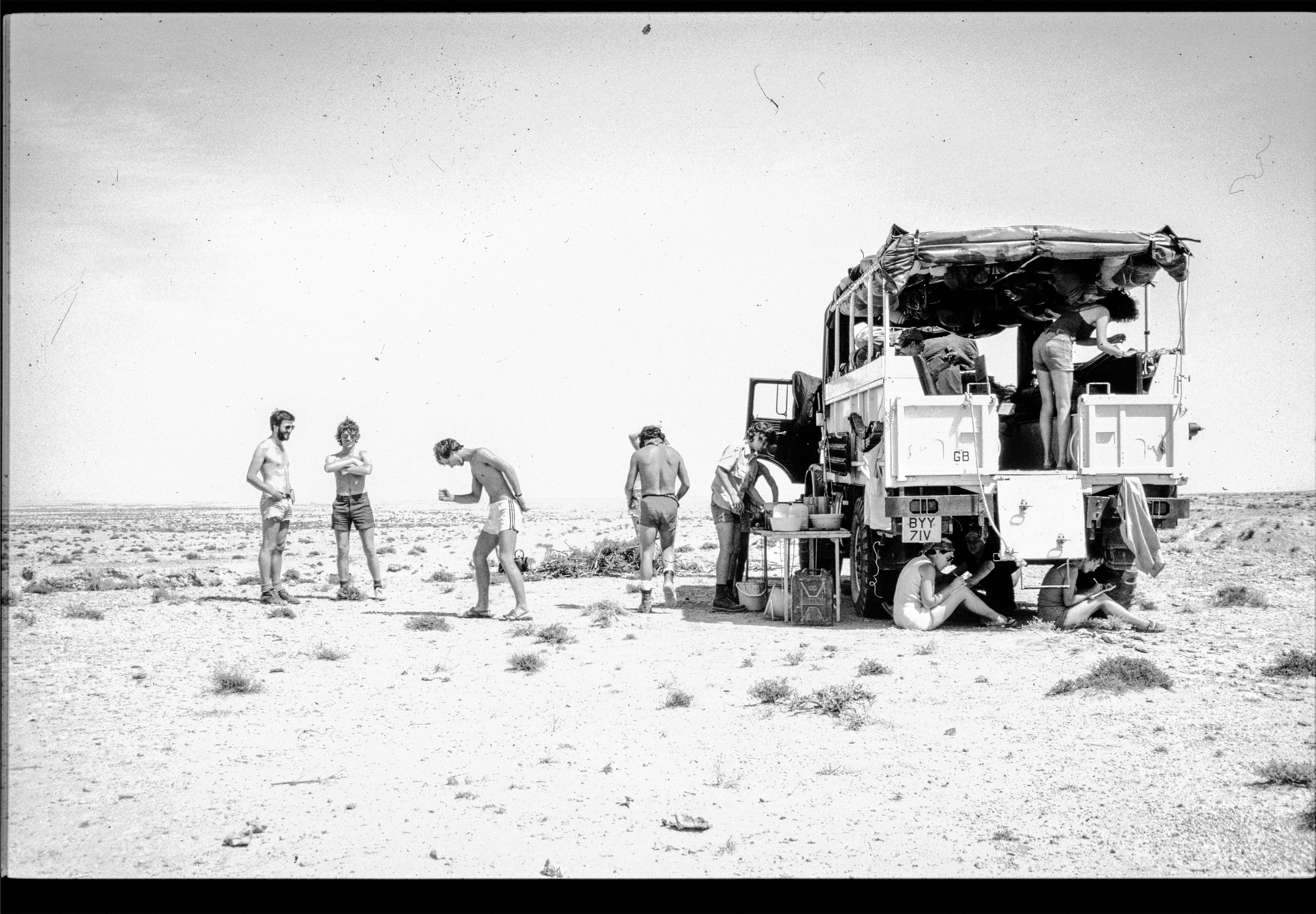 Desert Caravan: A Distant Crew and a Loaded Safari Truck on Arid Plains