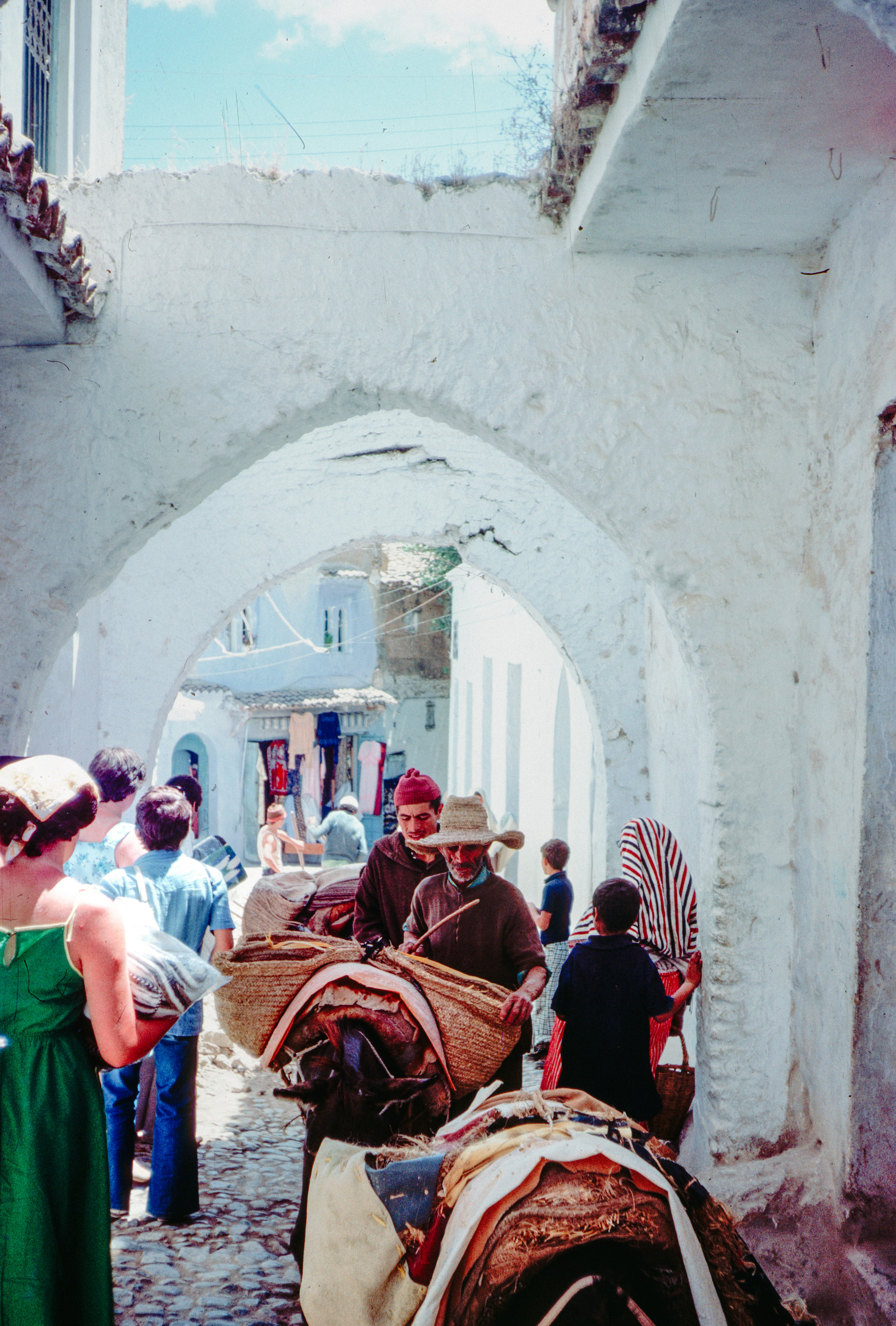 People walk through a white-arched alleyway carrying goods.