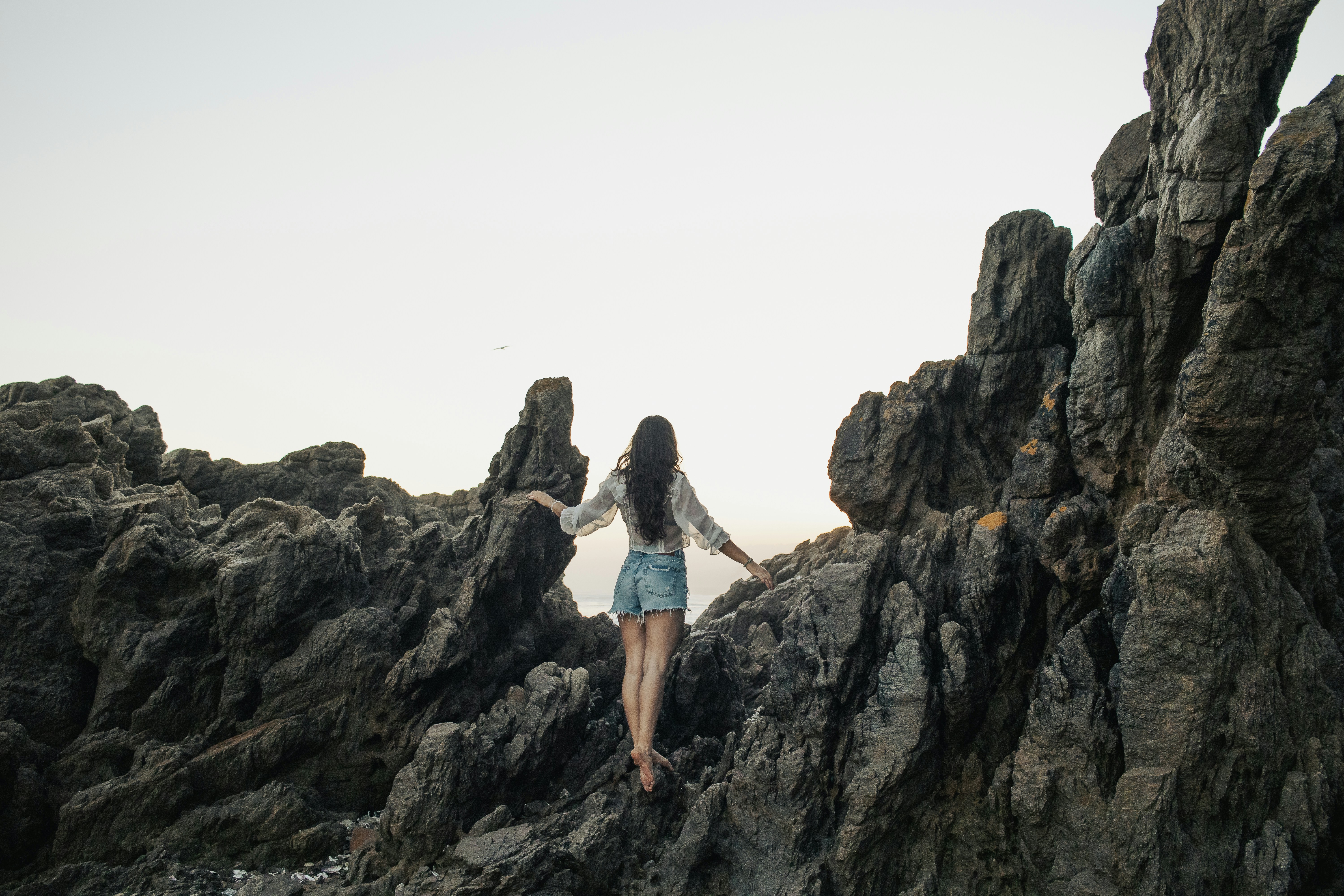 Cliffside Courage: Woman Steps Between Sea-streaked Rocks