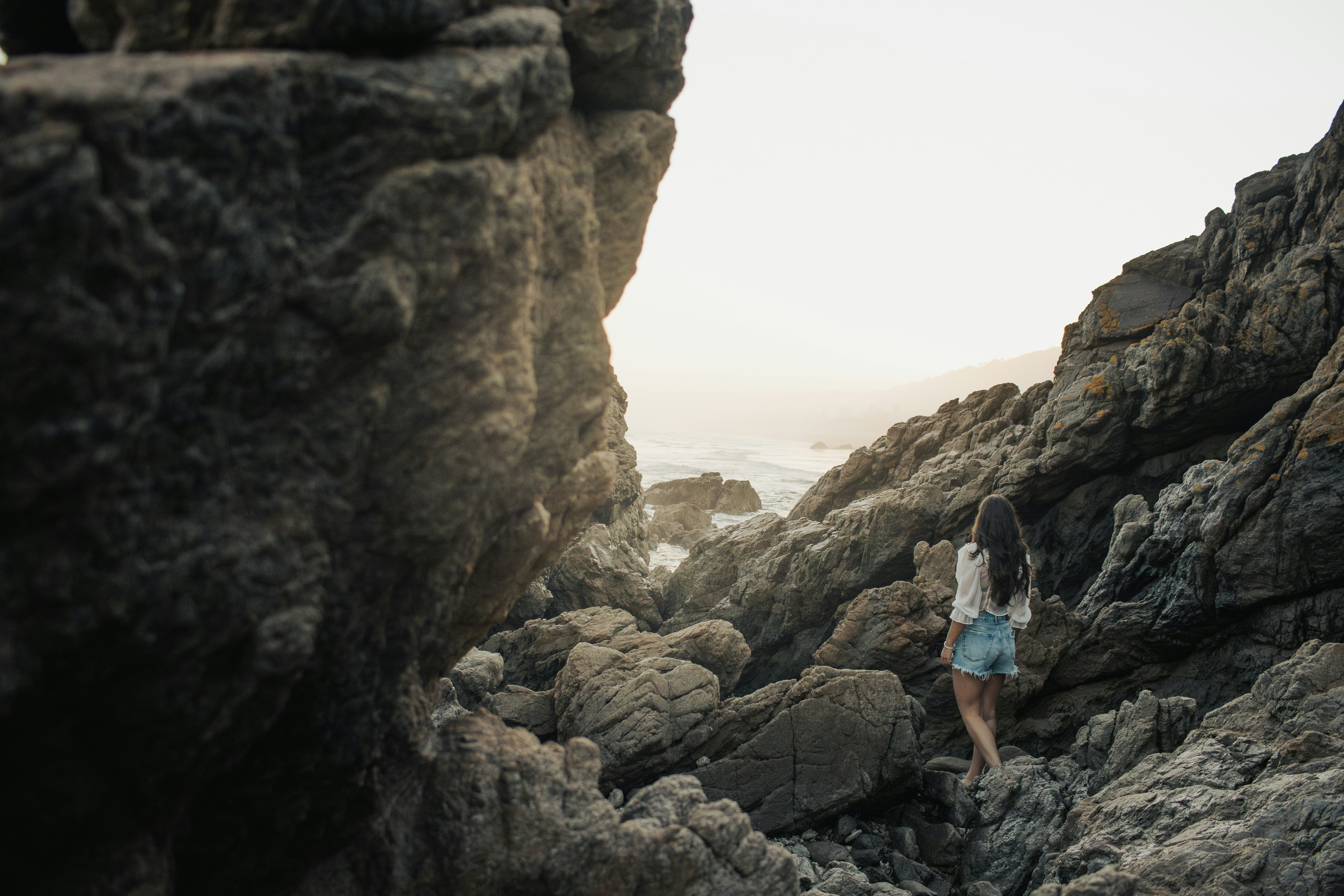 Stranded Between Giants: A solitary figure among jagged cliffs at shore