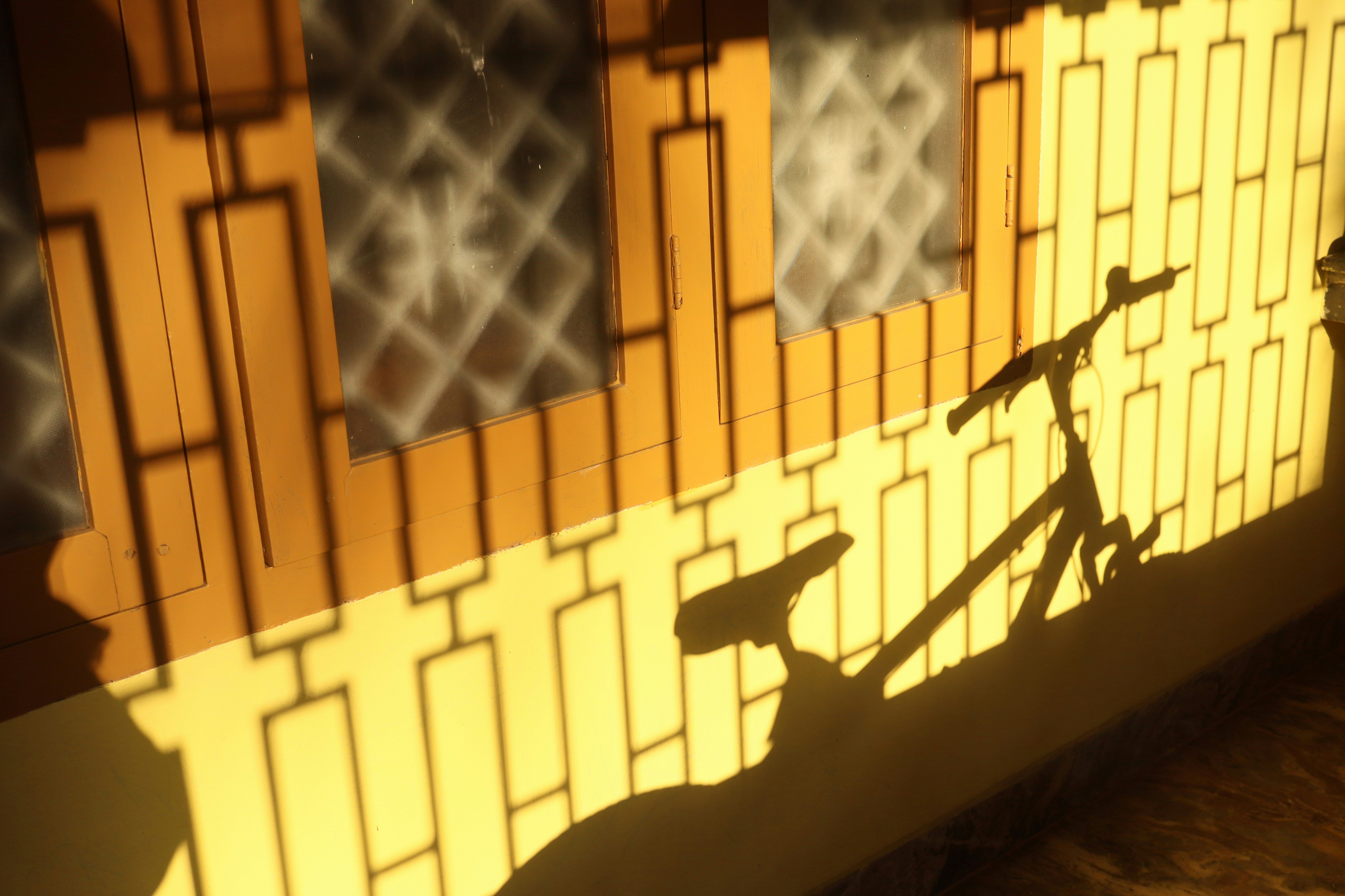 Muted sunset scene with a bicycle shadow cast on a yellow geometric wall, creating strong diagonal lines and warm tones.