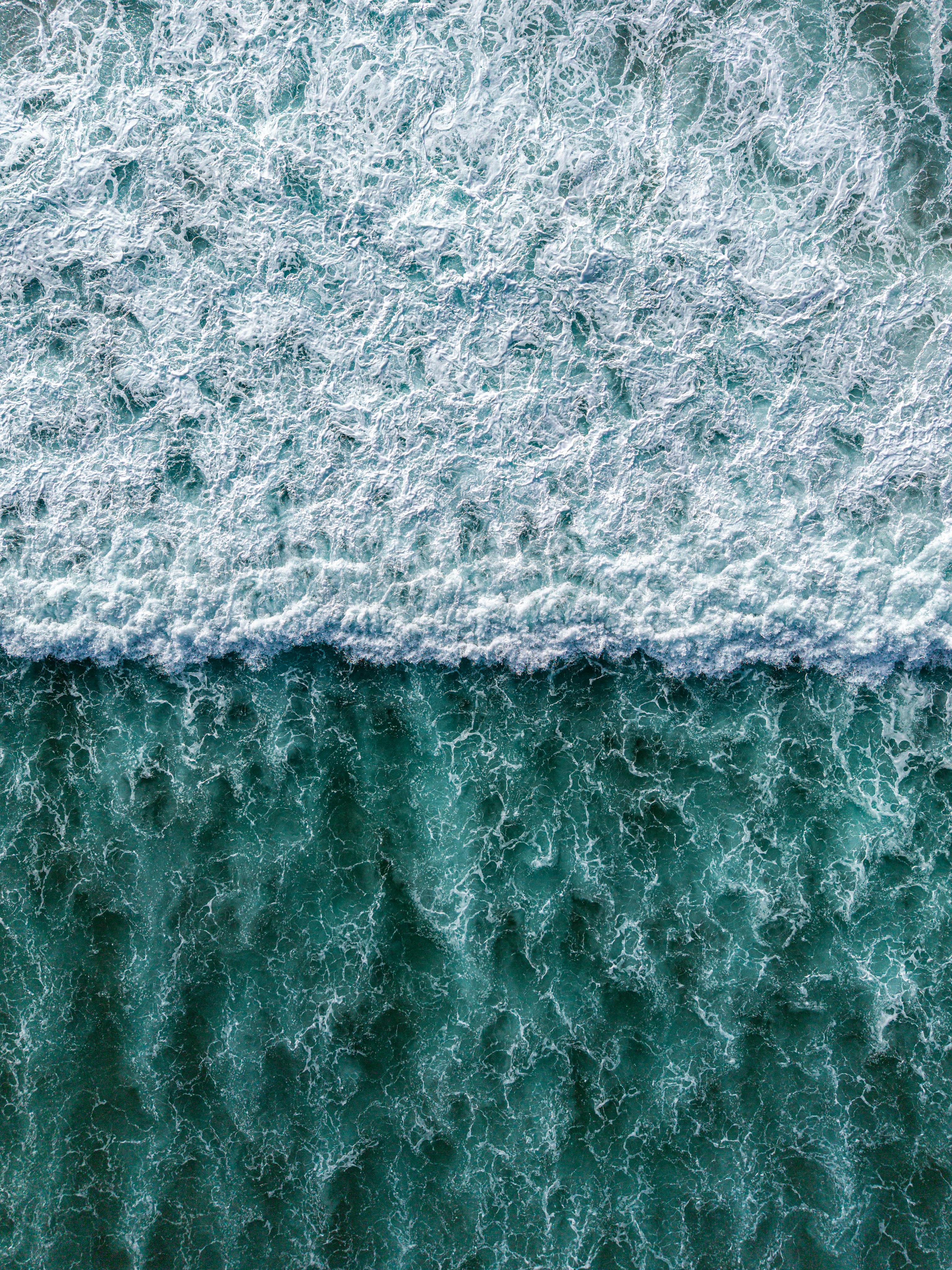 Aerial view of foamy ocean waves meeting turquoise water.