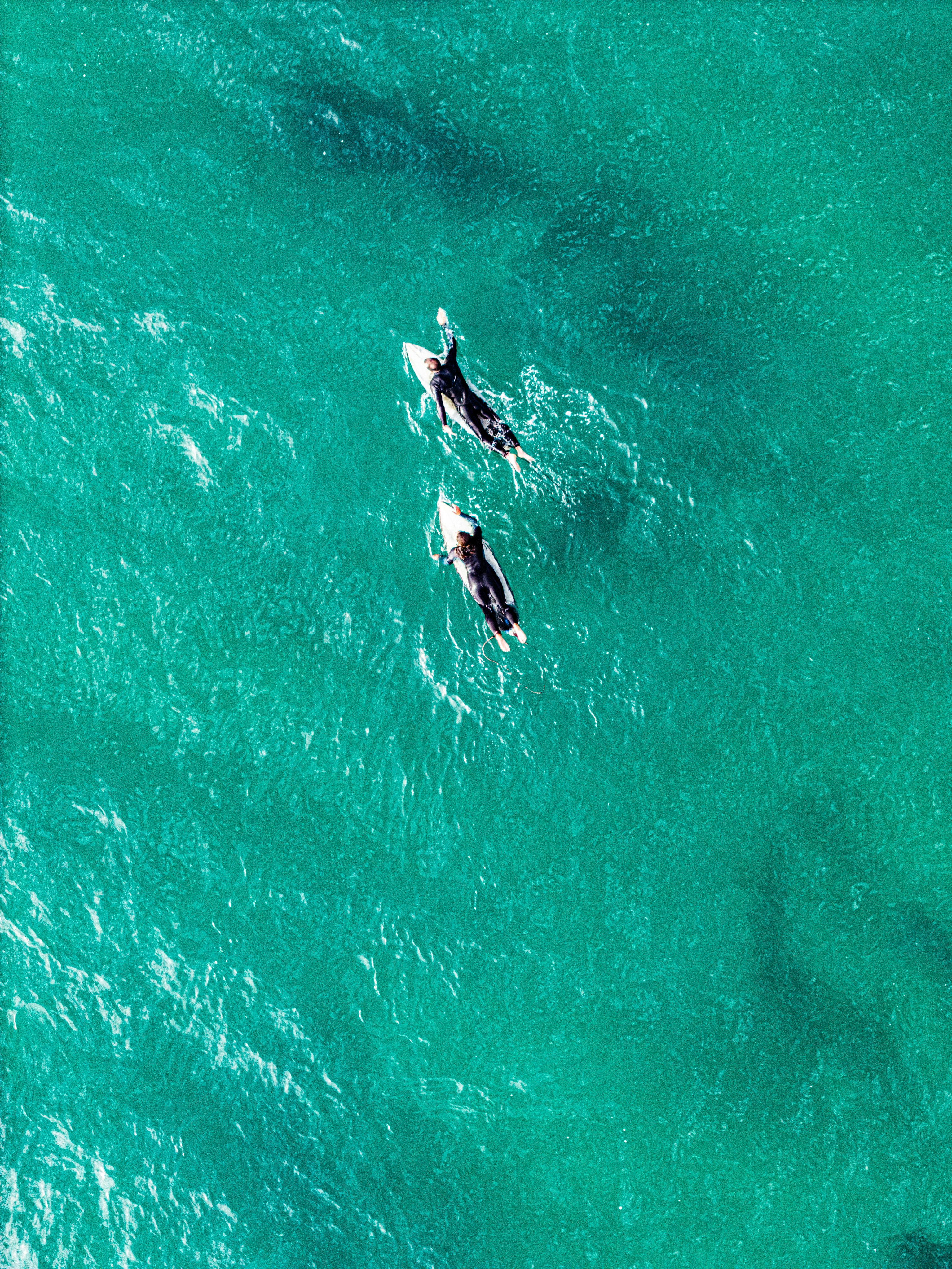 Two surfers glide through emerald calm from a bird’s-eye view