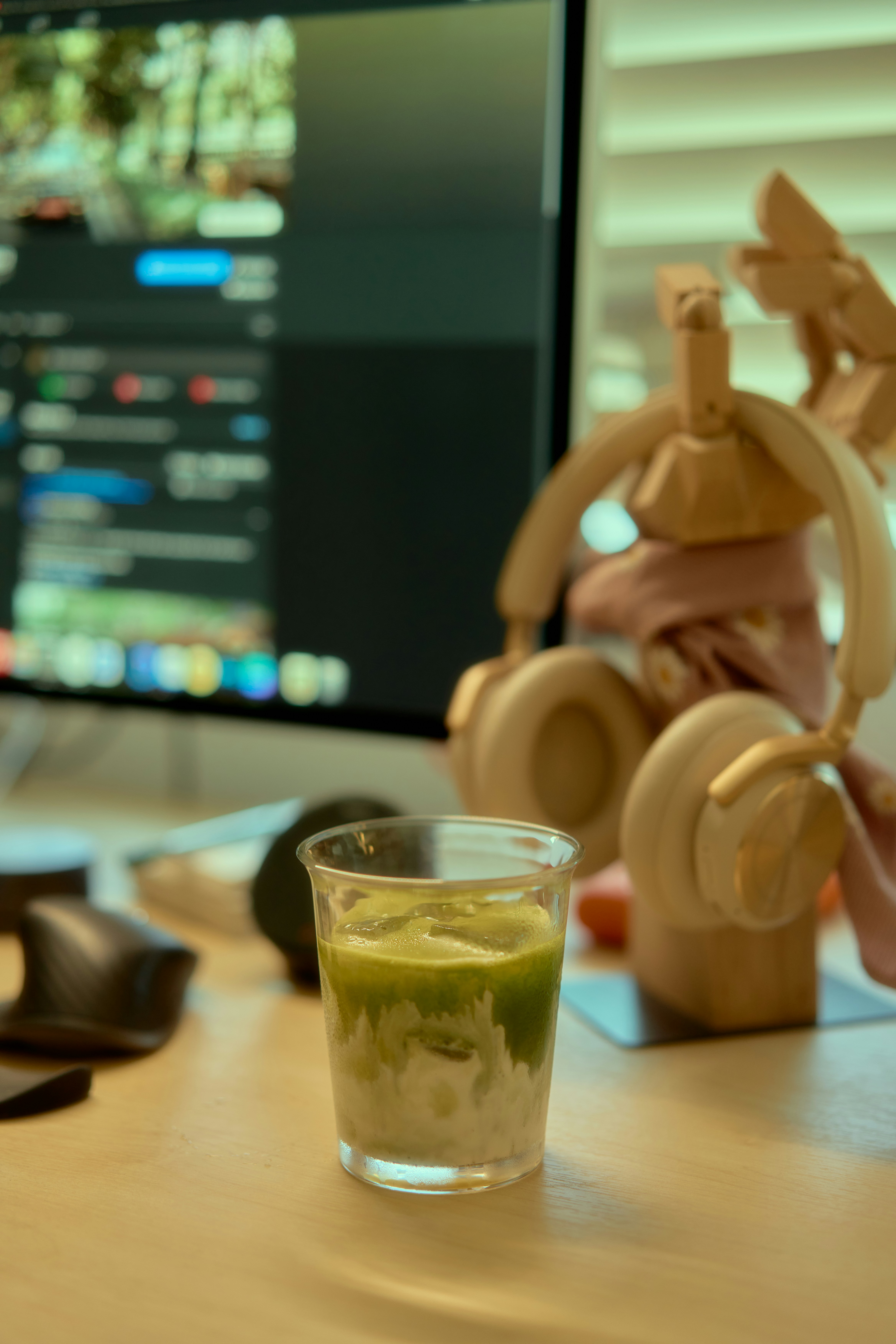 Green-tinged latte on a wooden desk with a blurred monitor and wooden headphone stand in the background