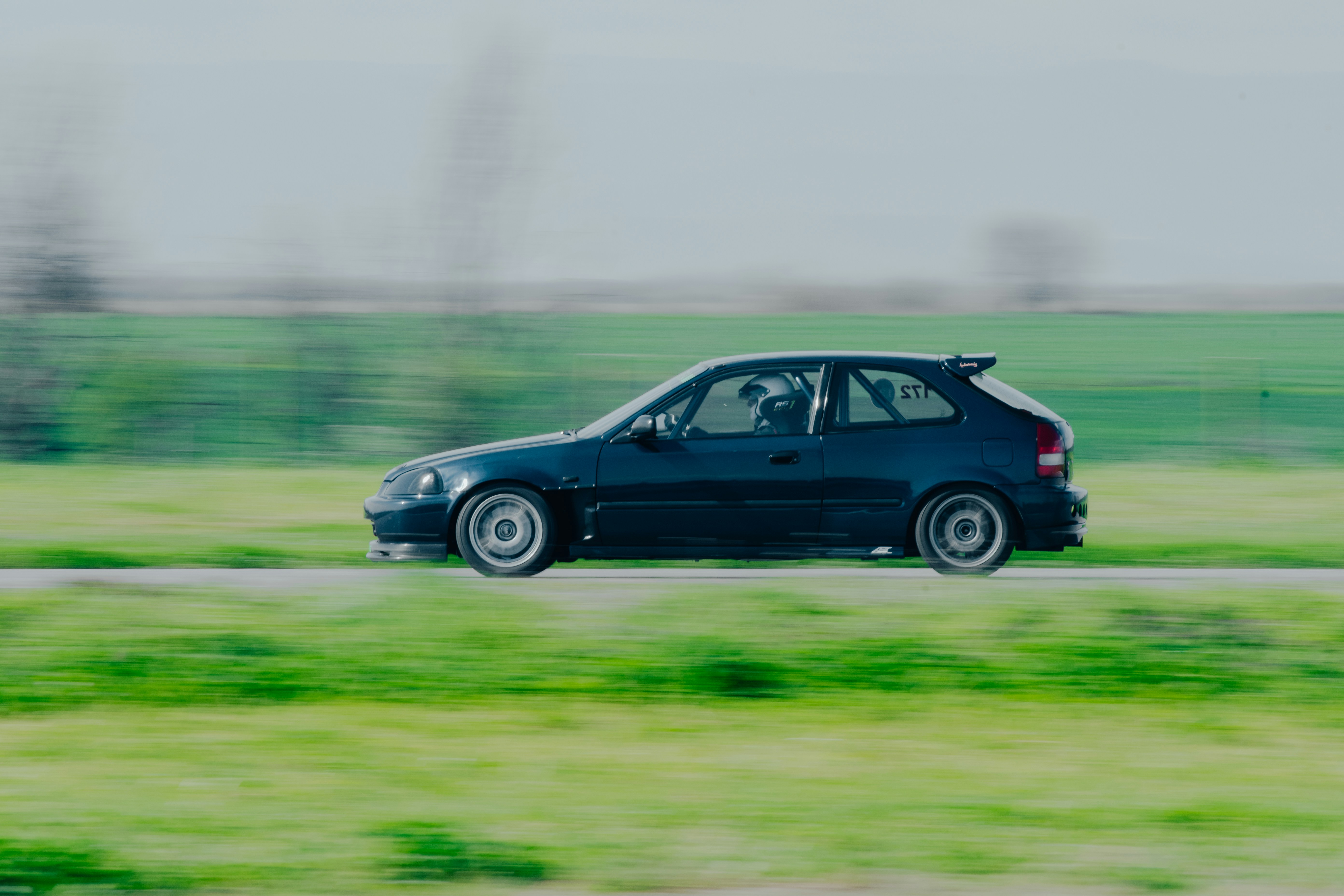 Midfield Blue: a lone hatchback in smooth sprint past green fields