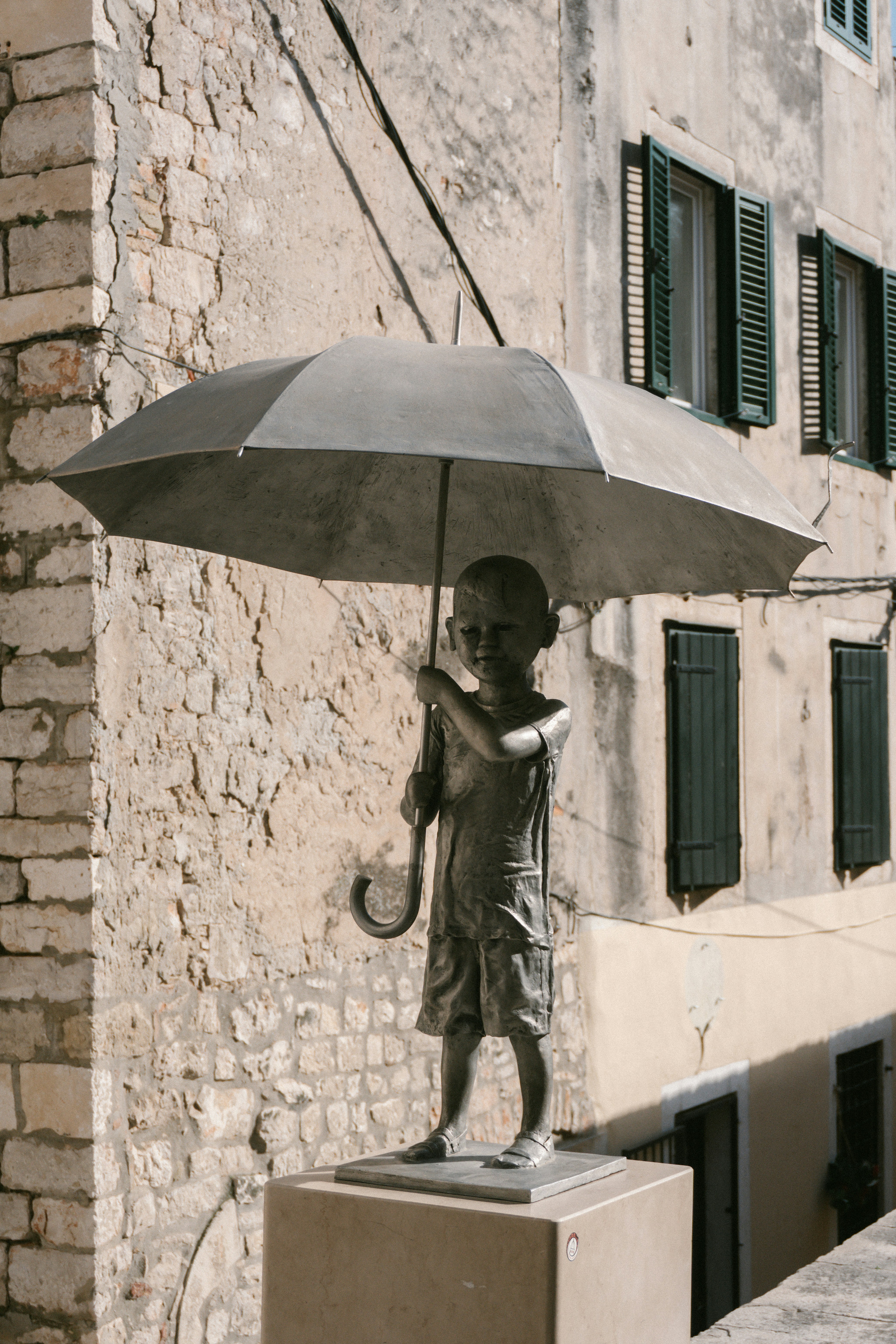 Umbrella Guardian: A Bronze Boy Stands Watch in Aegean Light