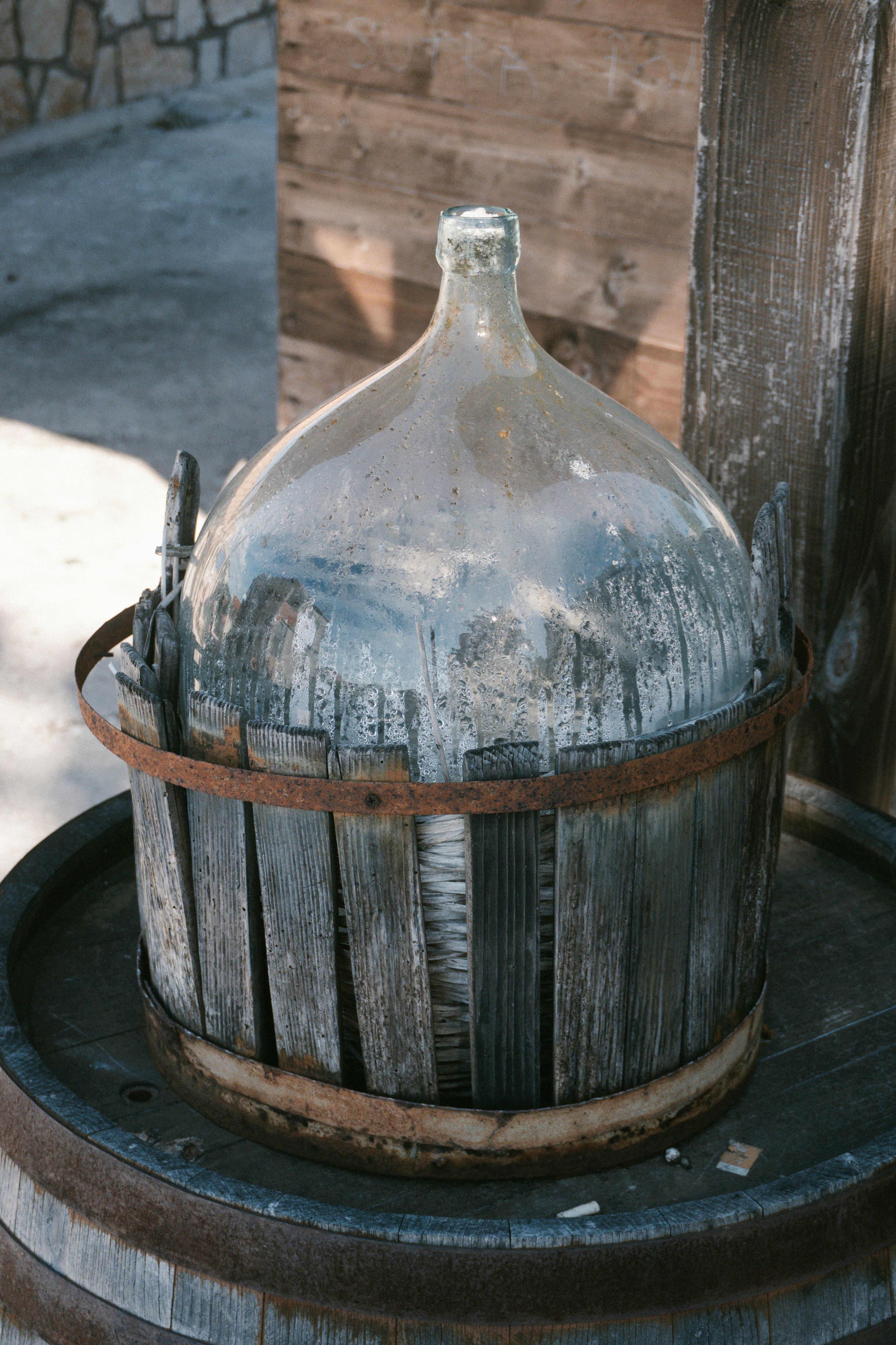 Weathered Jug Crowned by Time: A Vintage Glass Demijohn in a Rustic Wooden Cage