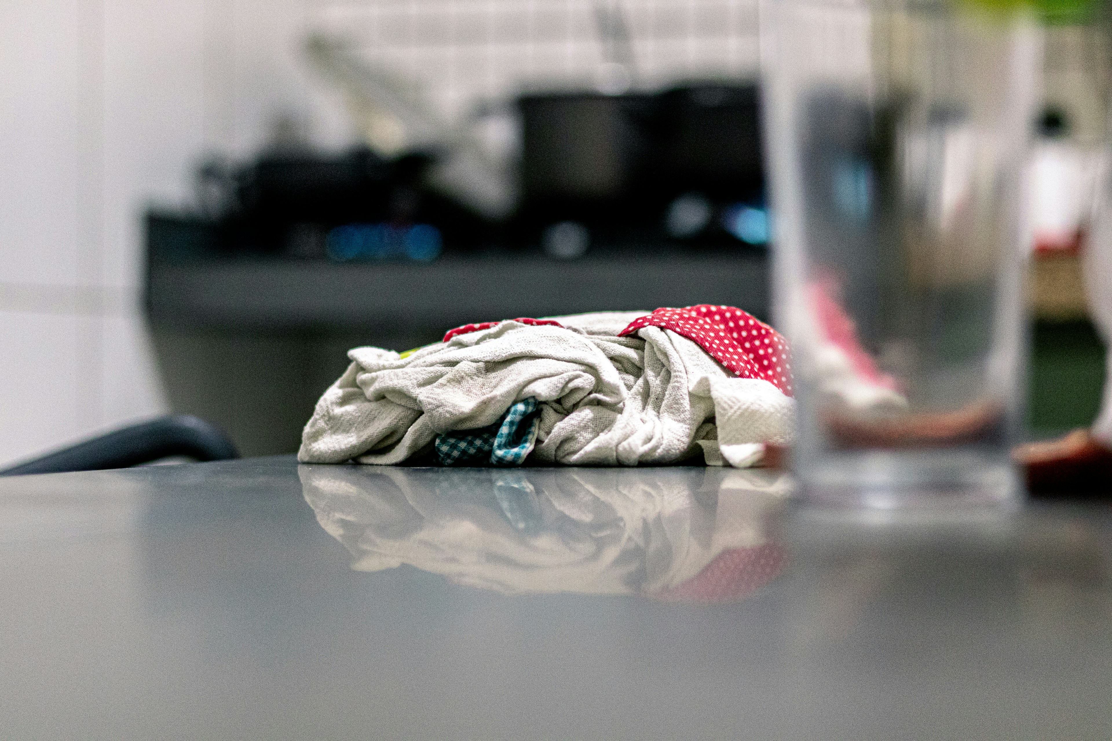 A pile of laundry sits on a reflective surface, hinting at domestic tasks.