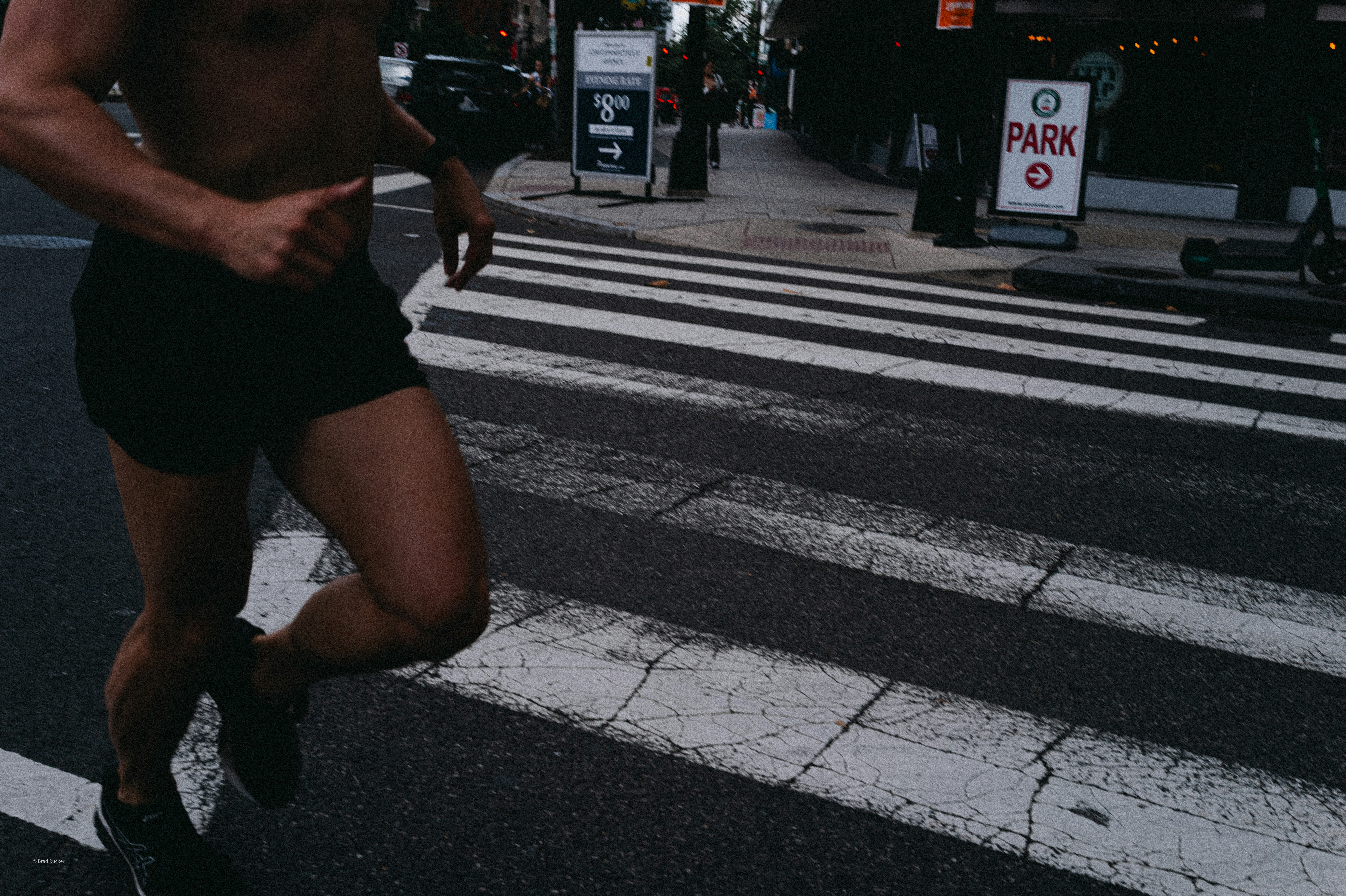 Man running shirtless across a city street crosswalk.