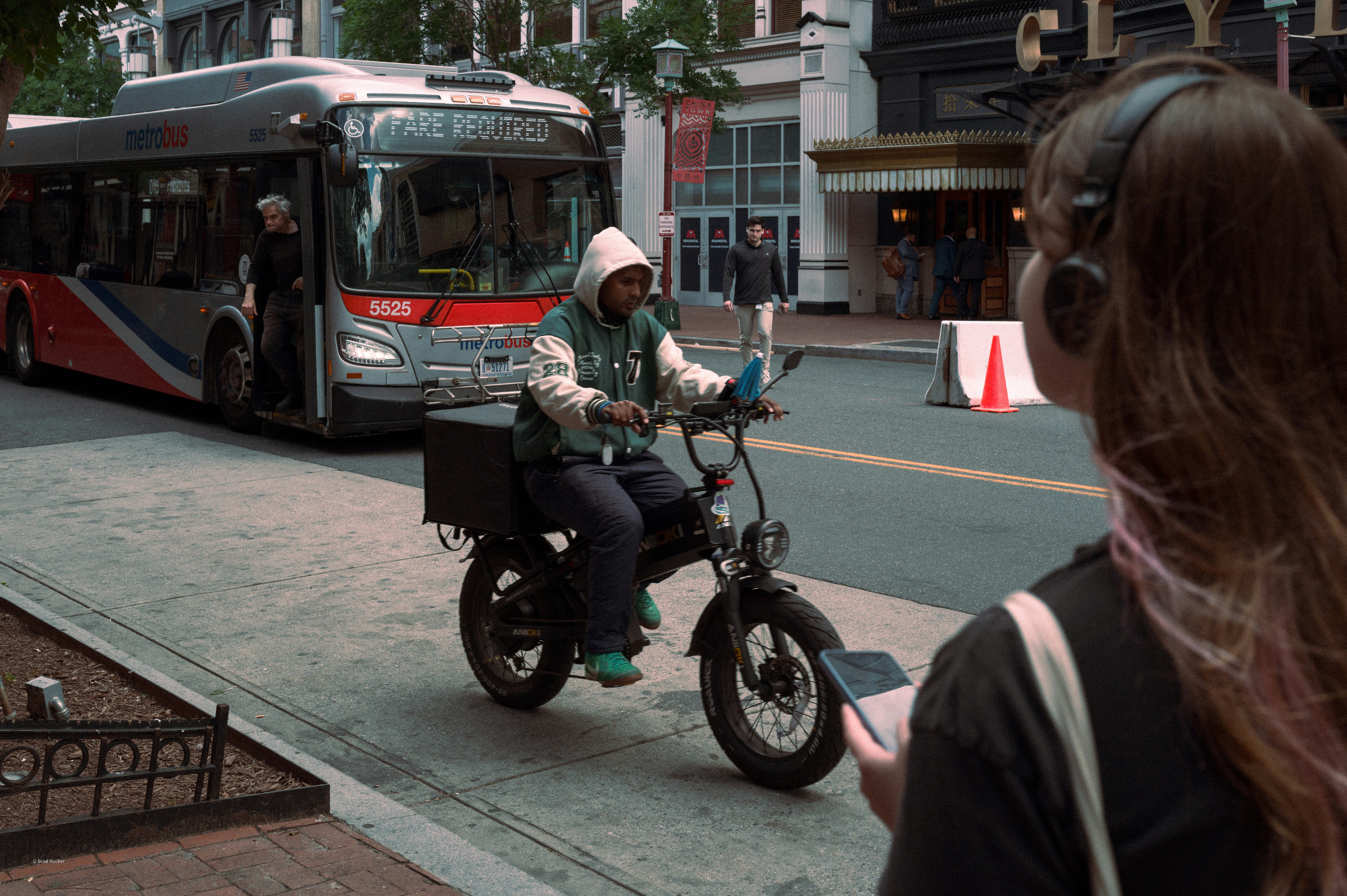City Street Encounter: rider on a motorcycle approaches as a passerby glances at a phone