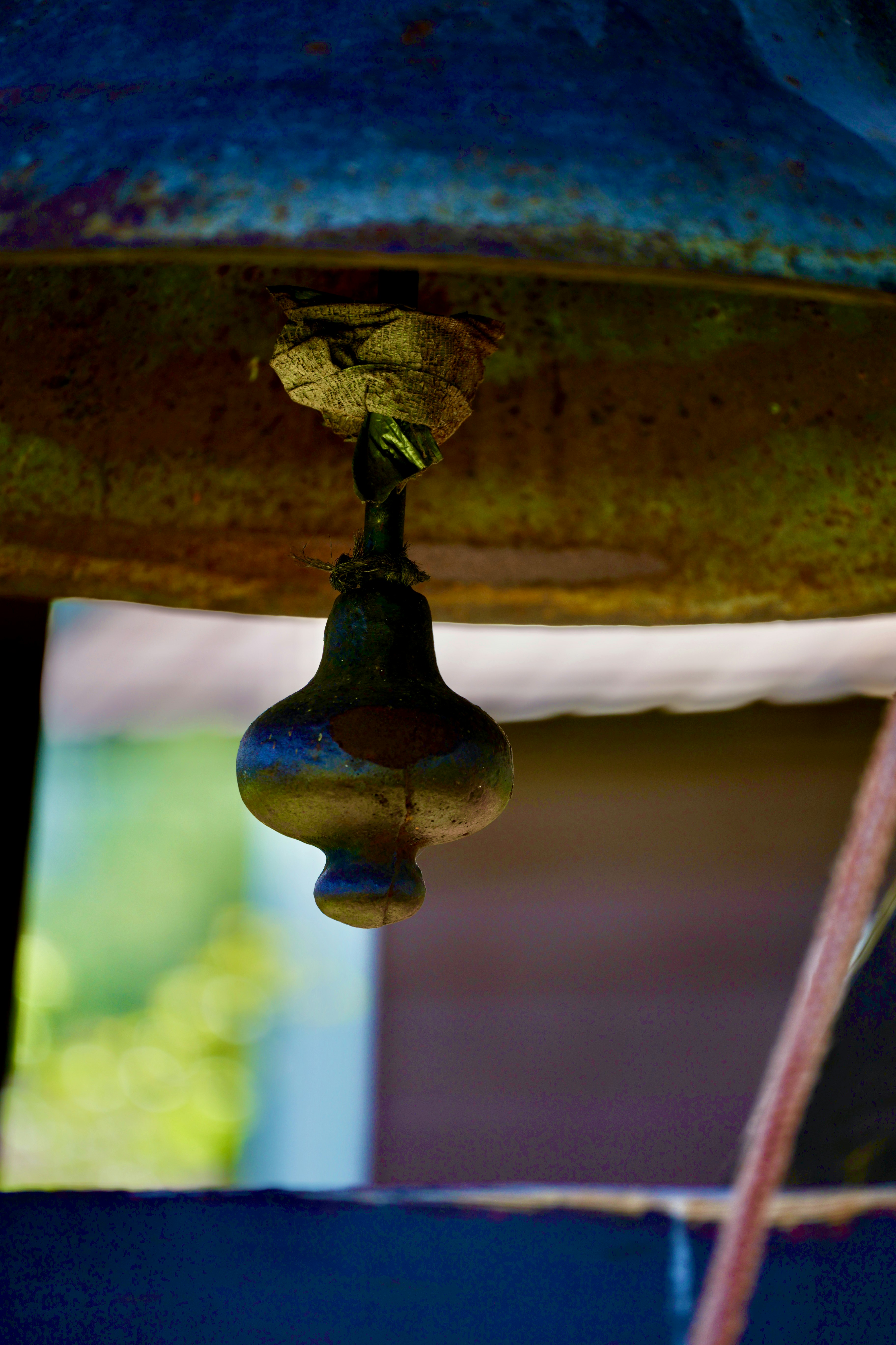 A weathered bell hammer and finial under a rusty blue bell