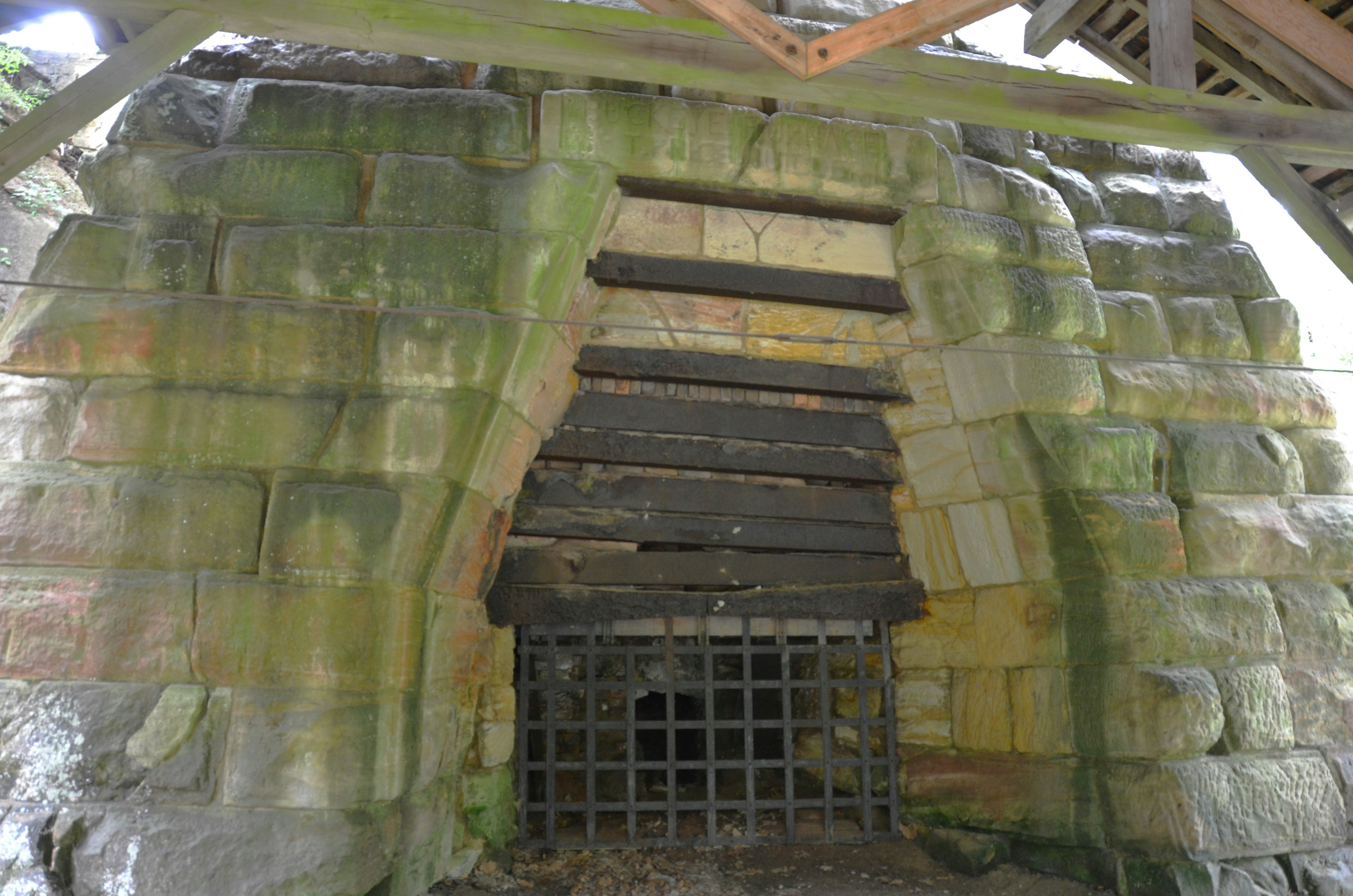  Moss-veiled kiln facade: weathered stone arch with iron grate