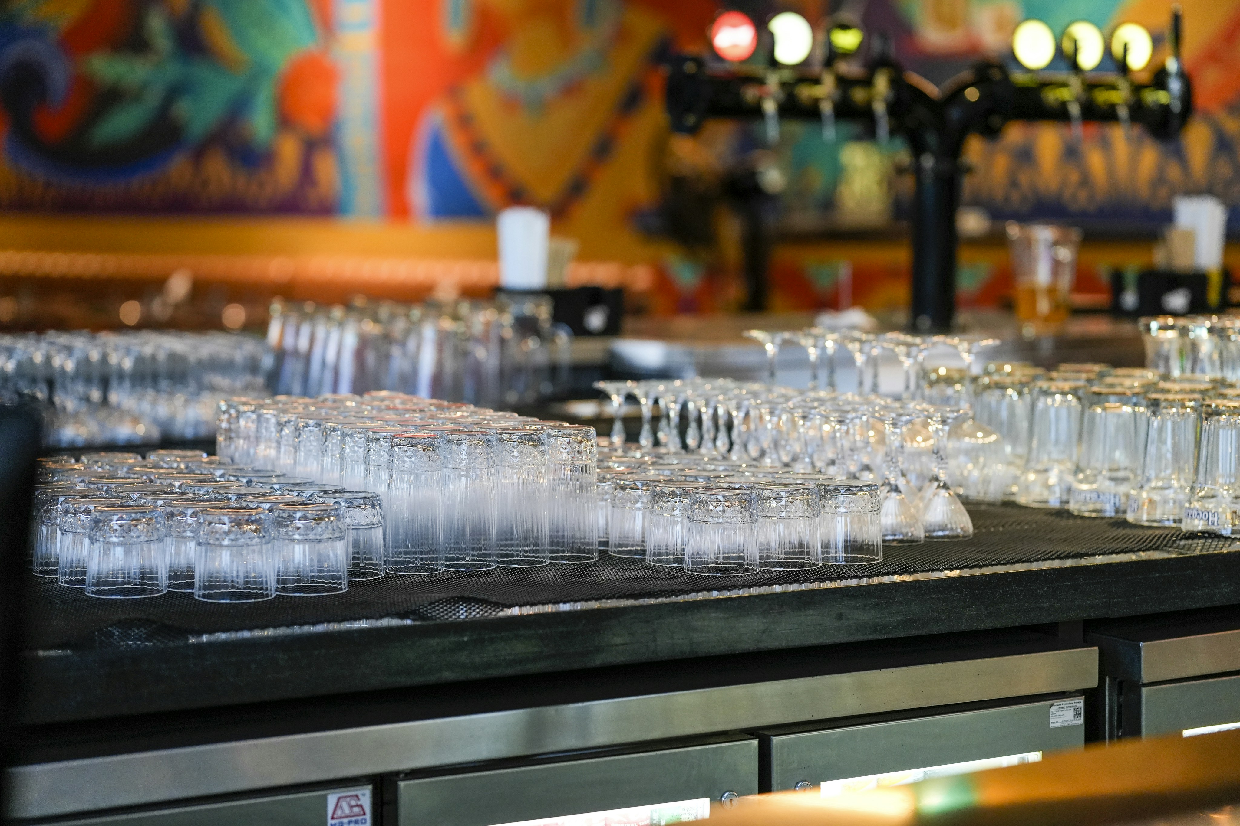 Many empty glasses on a bar counter with beer taps.