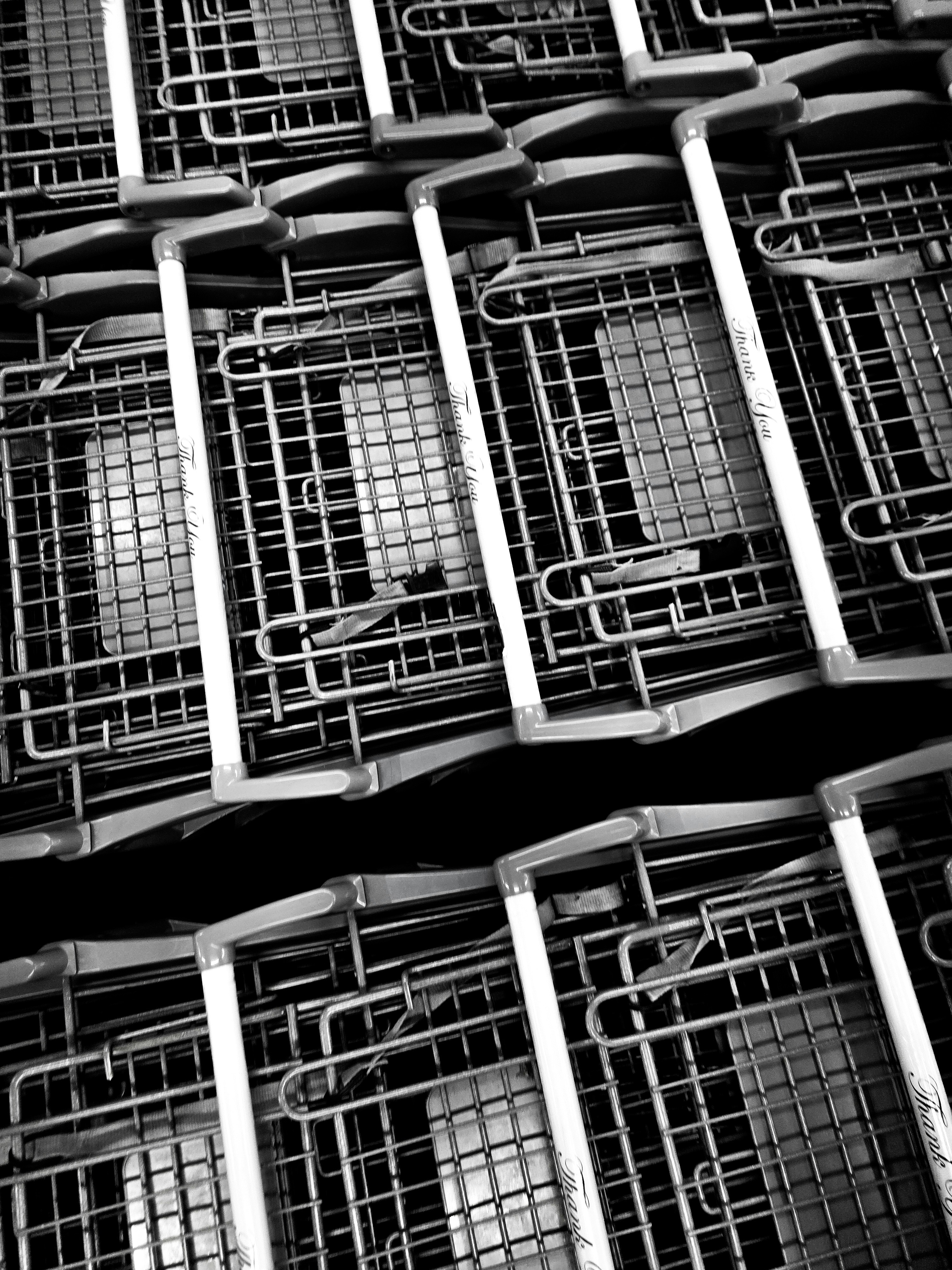 Monochrome shot of stacked metal shopping baskets compactly arranged, emphasizing their grids and handles to create an abstract urban texture.