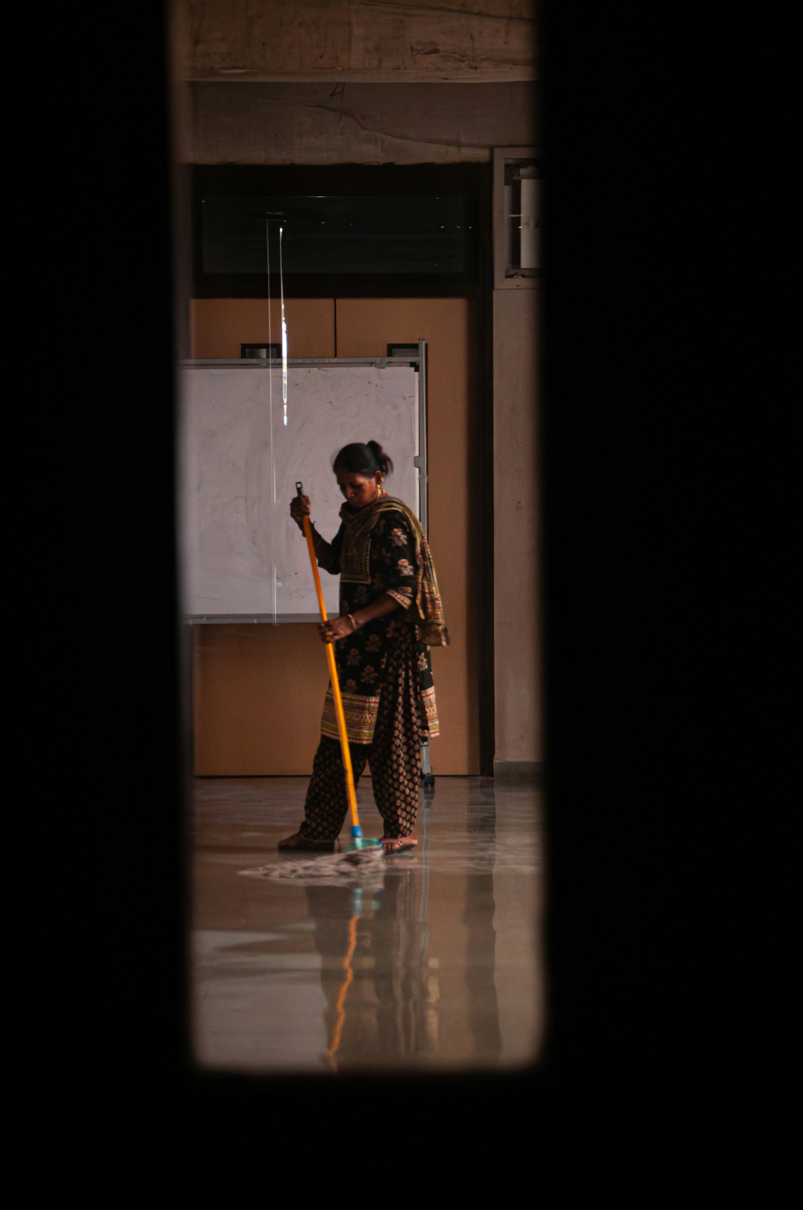Solemn Sweeping: A Attire-Clad Worker in Quiet Hall with a Long Mop
