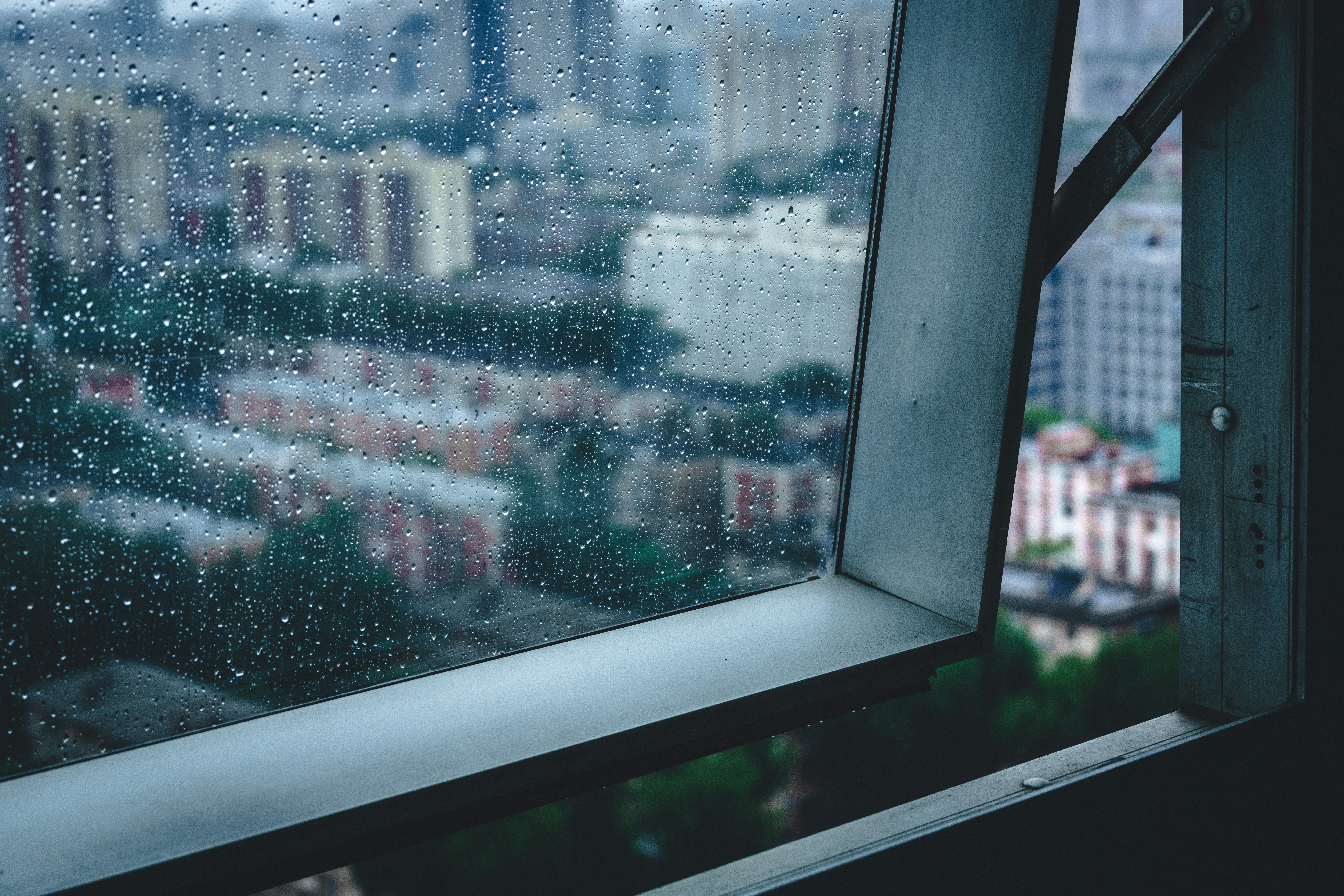 Raindrops on a window overlooking a blurry cityscape.