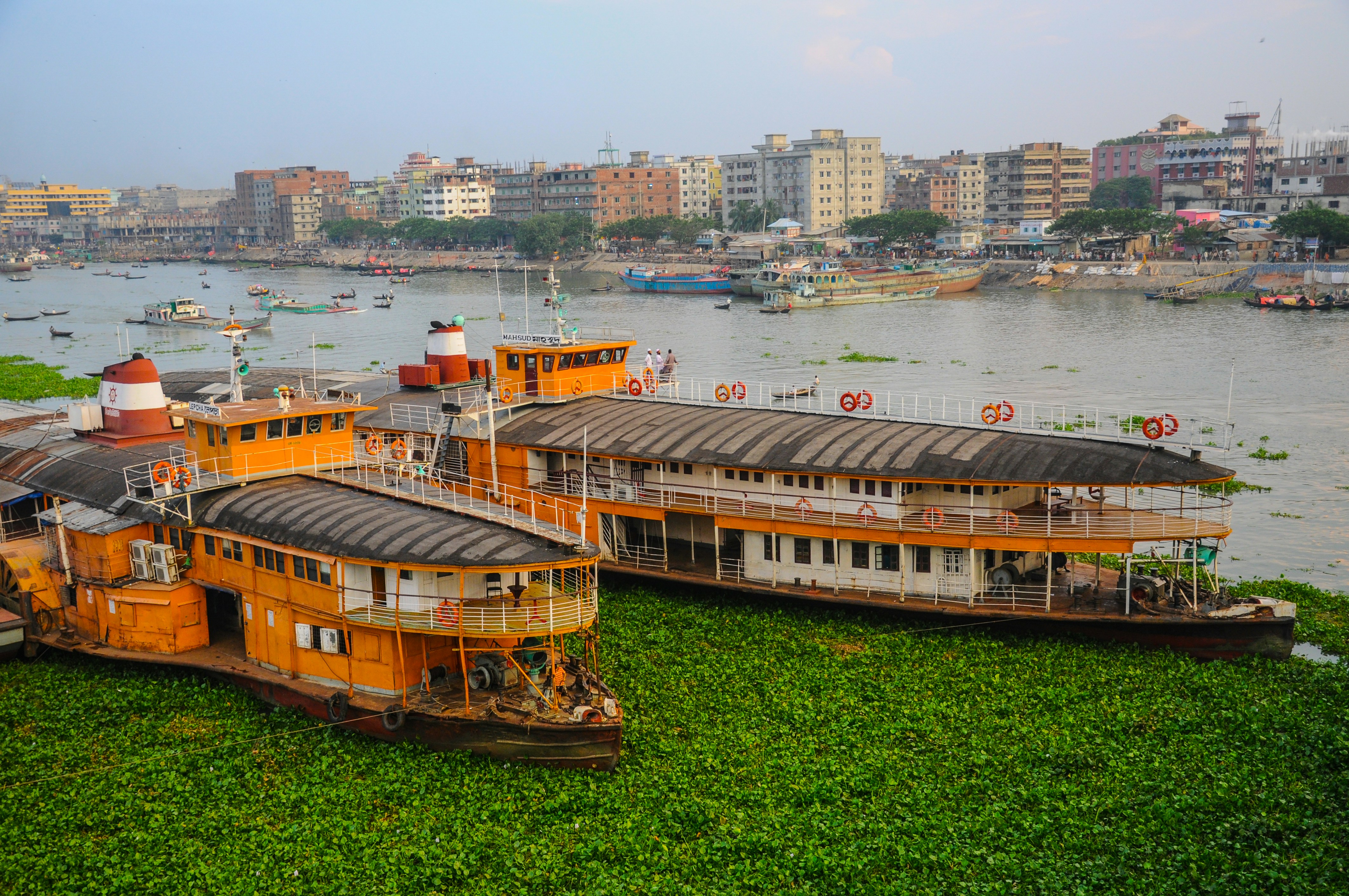 Historic paddle steamers on the Buriganga River in Dhaka. Historic paddle steamers, often known as Rocket Steamers, docked on the Buriganga River in Dhaka, Bangladesh. Surrounded by water hyacinth and busy river traffic, the vessels reflect the city’s river transport heritage and the environmental pressure on one of Dhaka’s most important waterways.