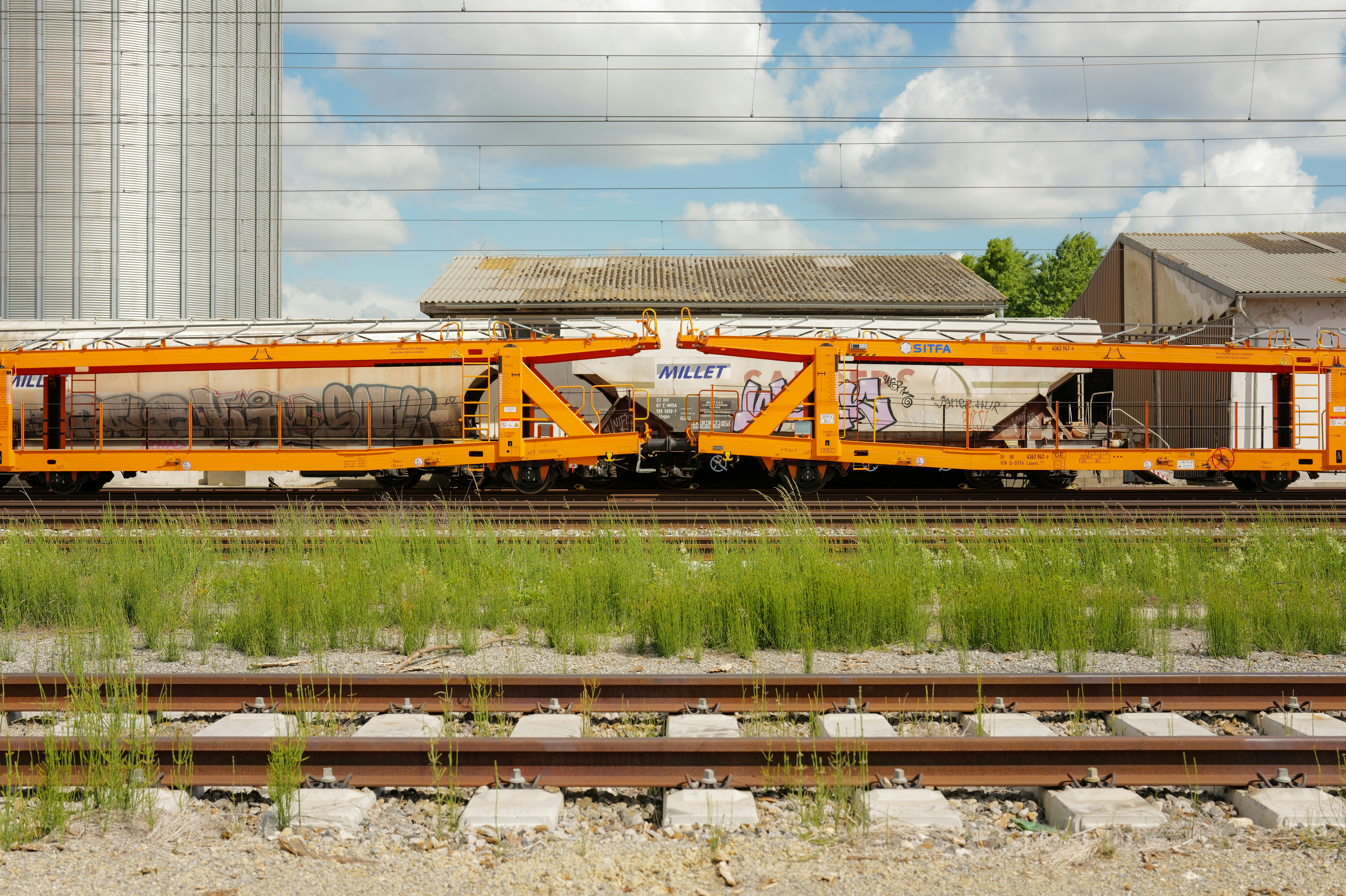 Orange cargo train carries a sunlit row of graffiti beneath industrial silhouettes