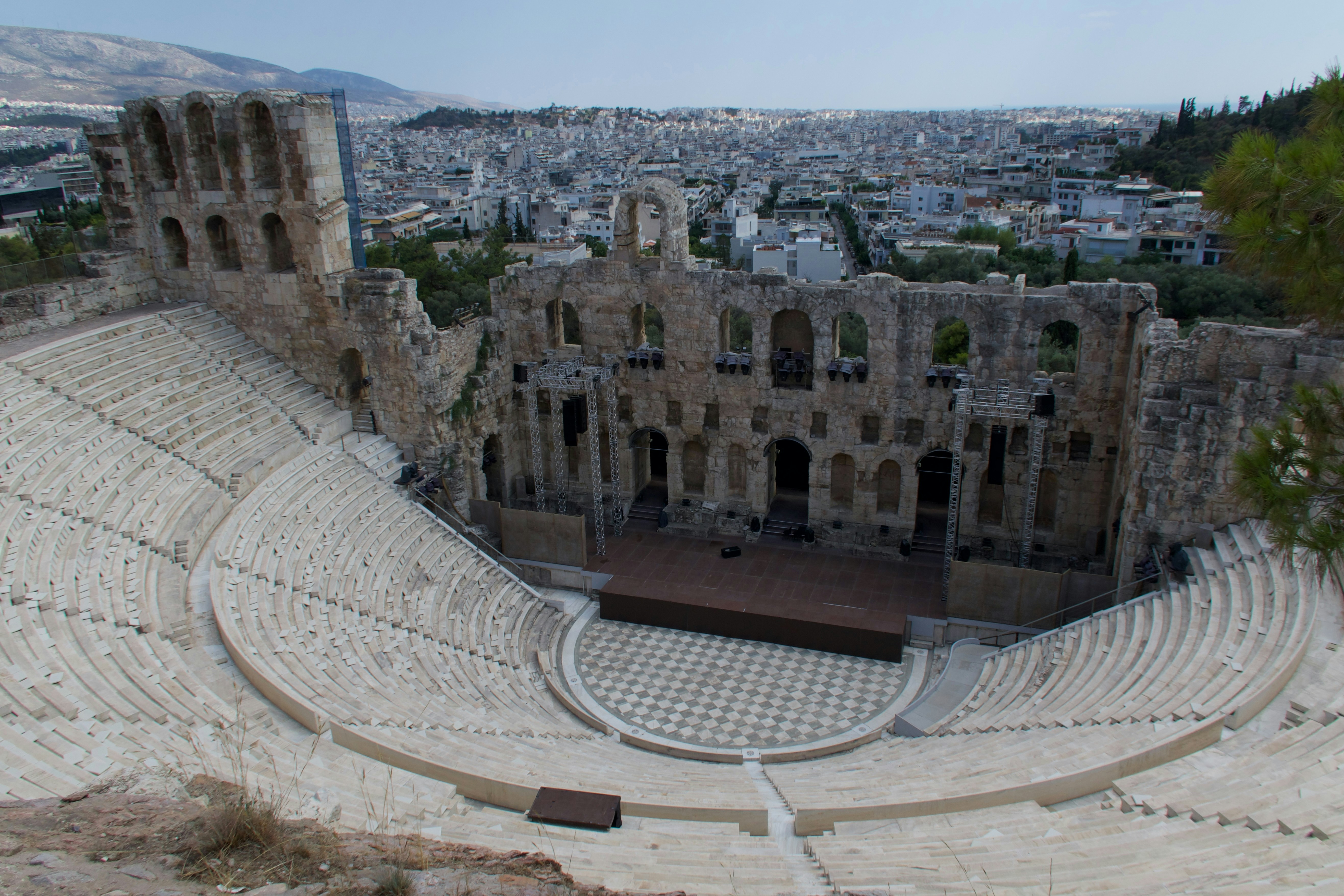 Sunlit ancient amphitheater: stone tiers and stage set against a hillside city