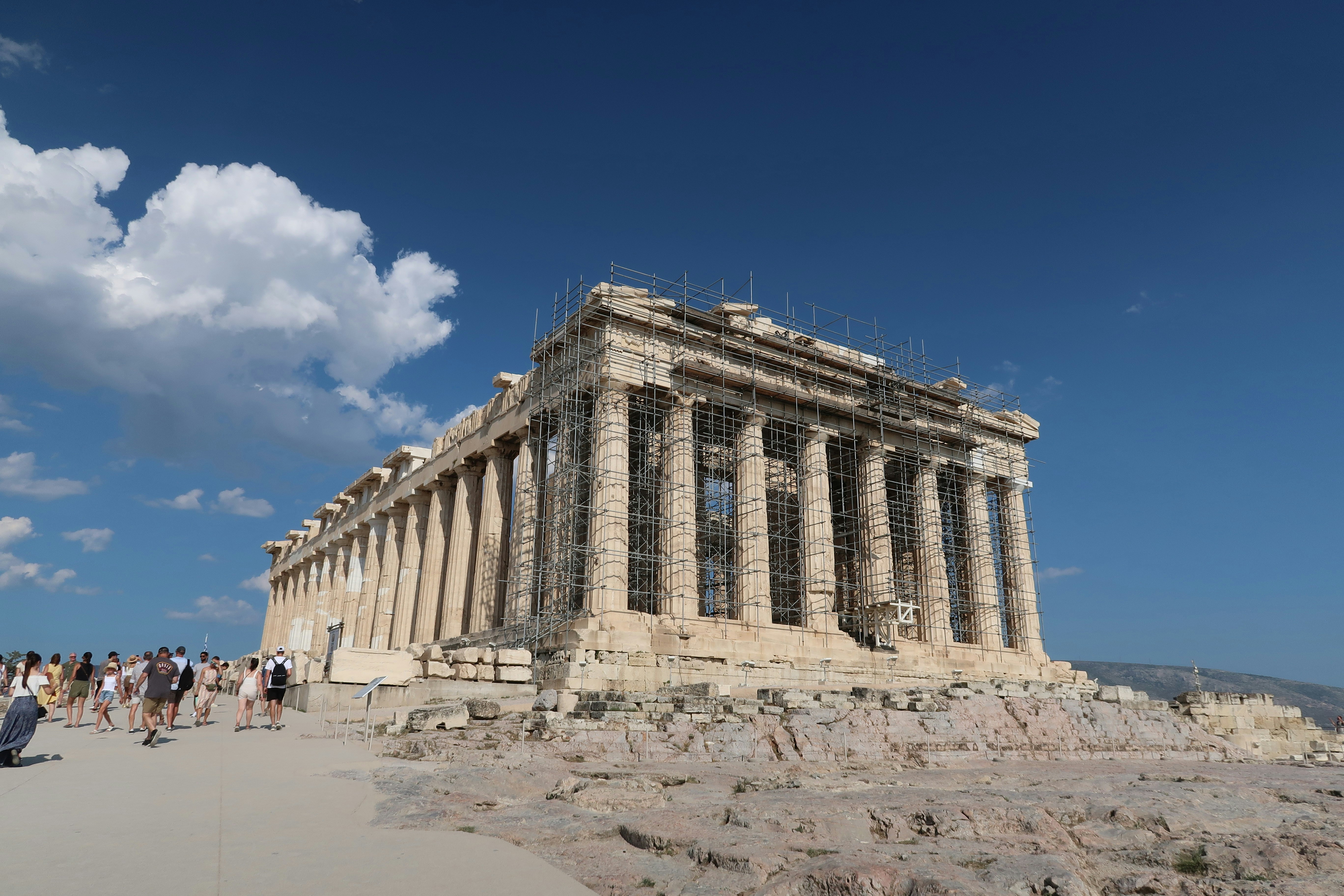 Ancient temple under bright Aegean sky, scaffolded for restoration