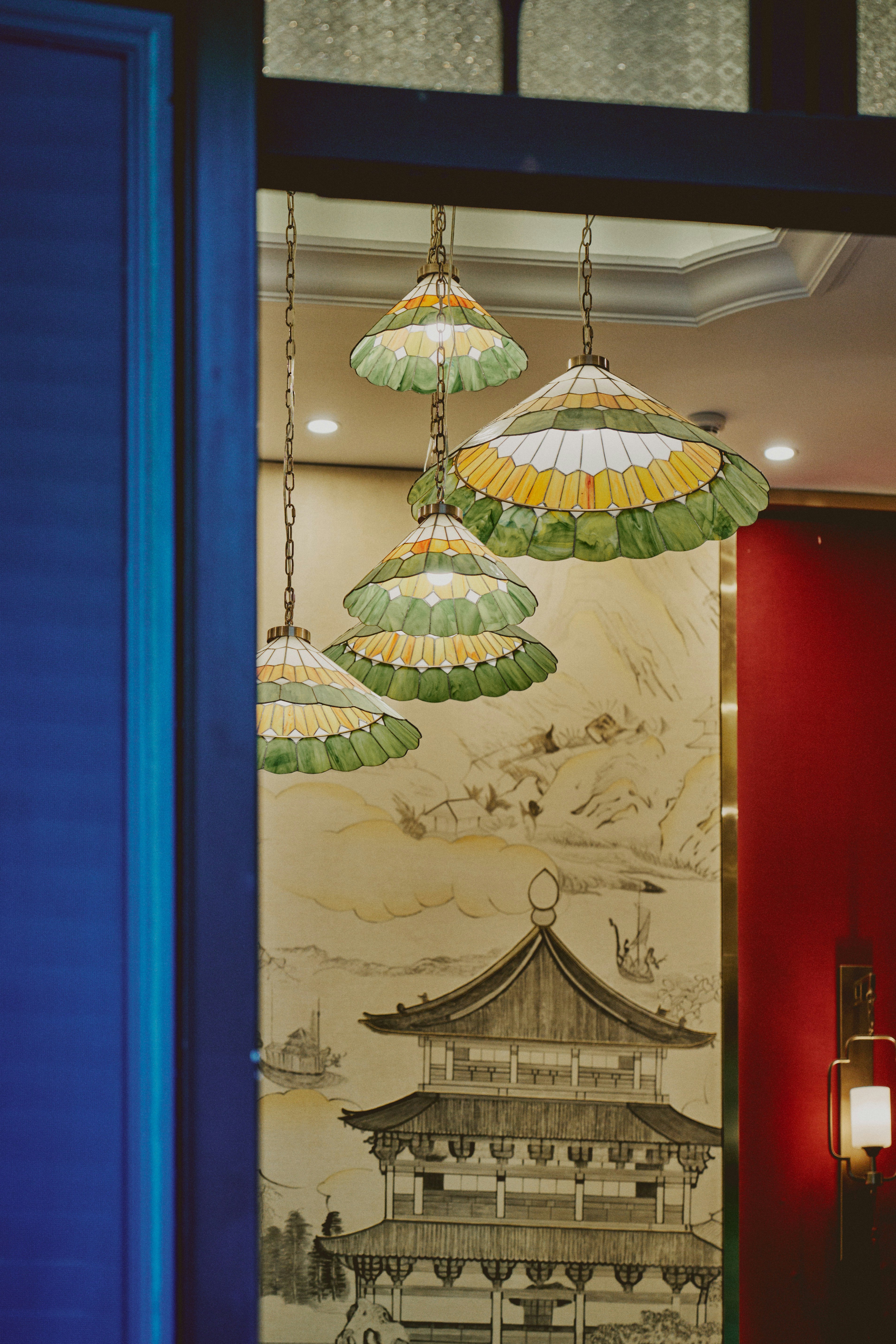 Green and yellow lamps hang above a traditional pagoda mural.