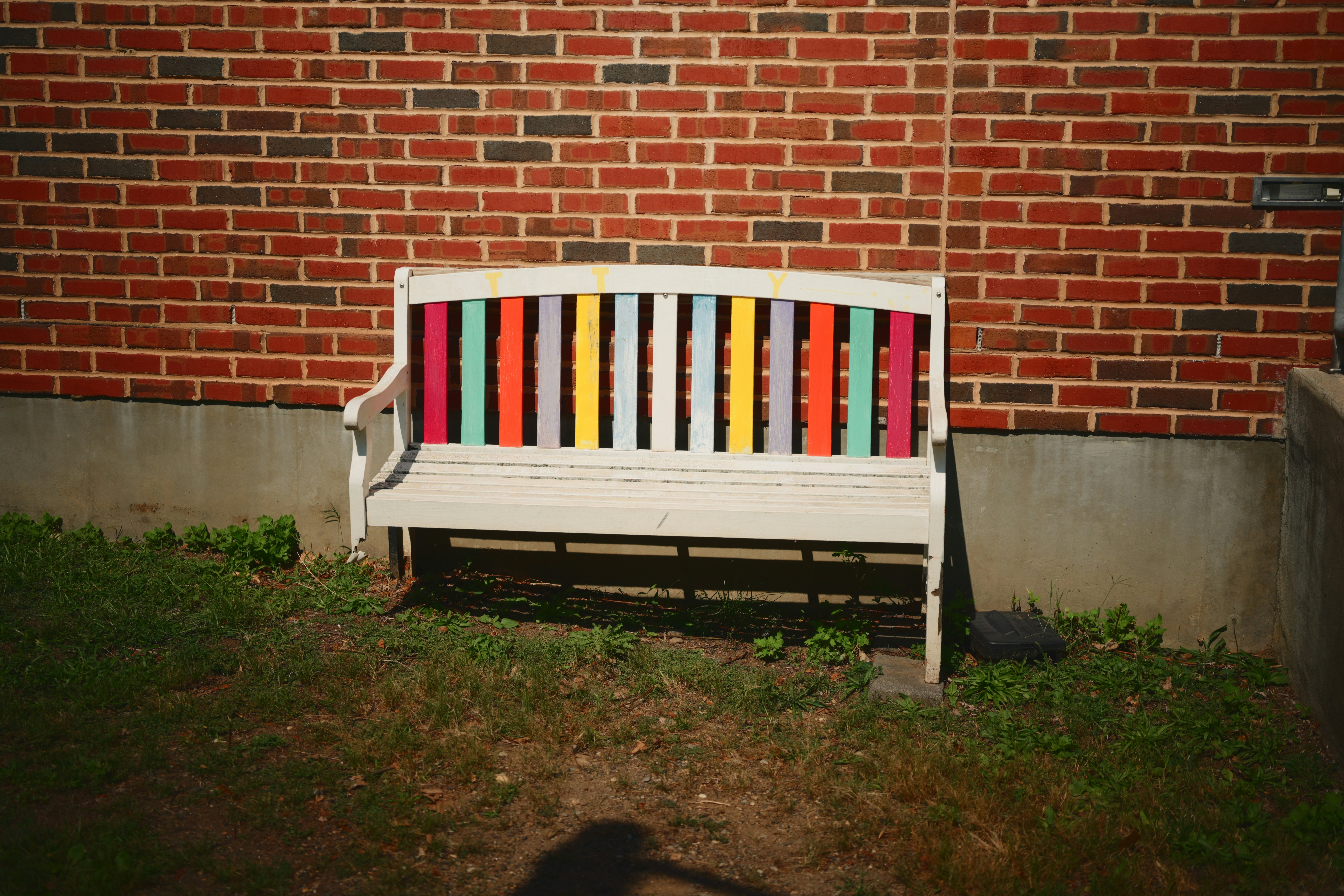 Multicolored Slats on a White Bench Against a Brick Wall