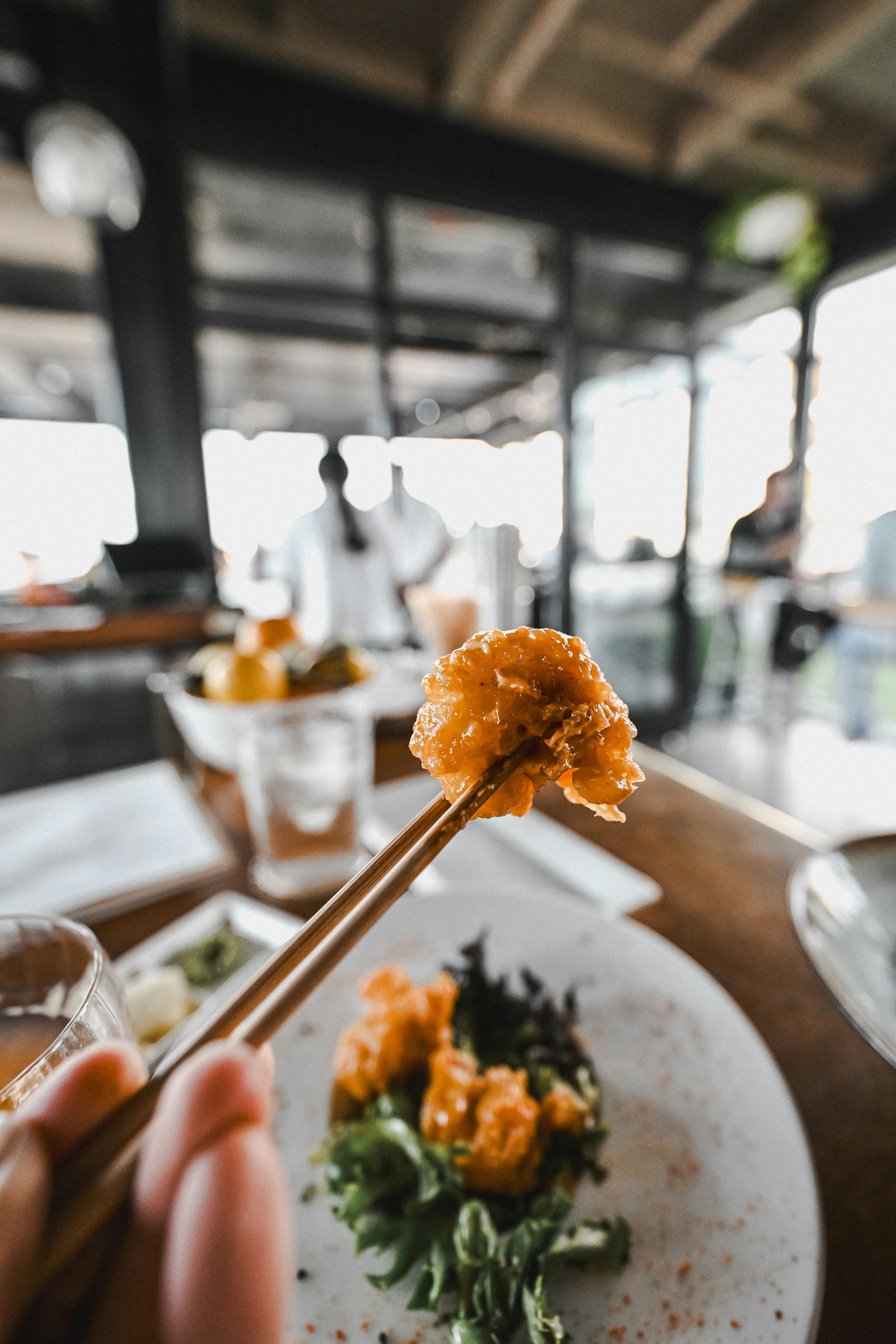 Hand holding fried tempura with chopsticks in a restaurant.