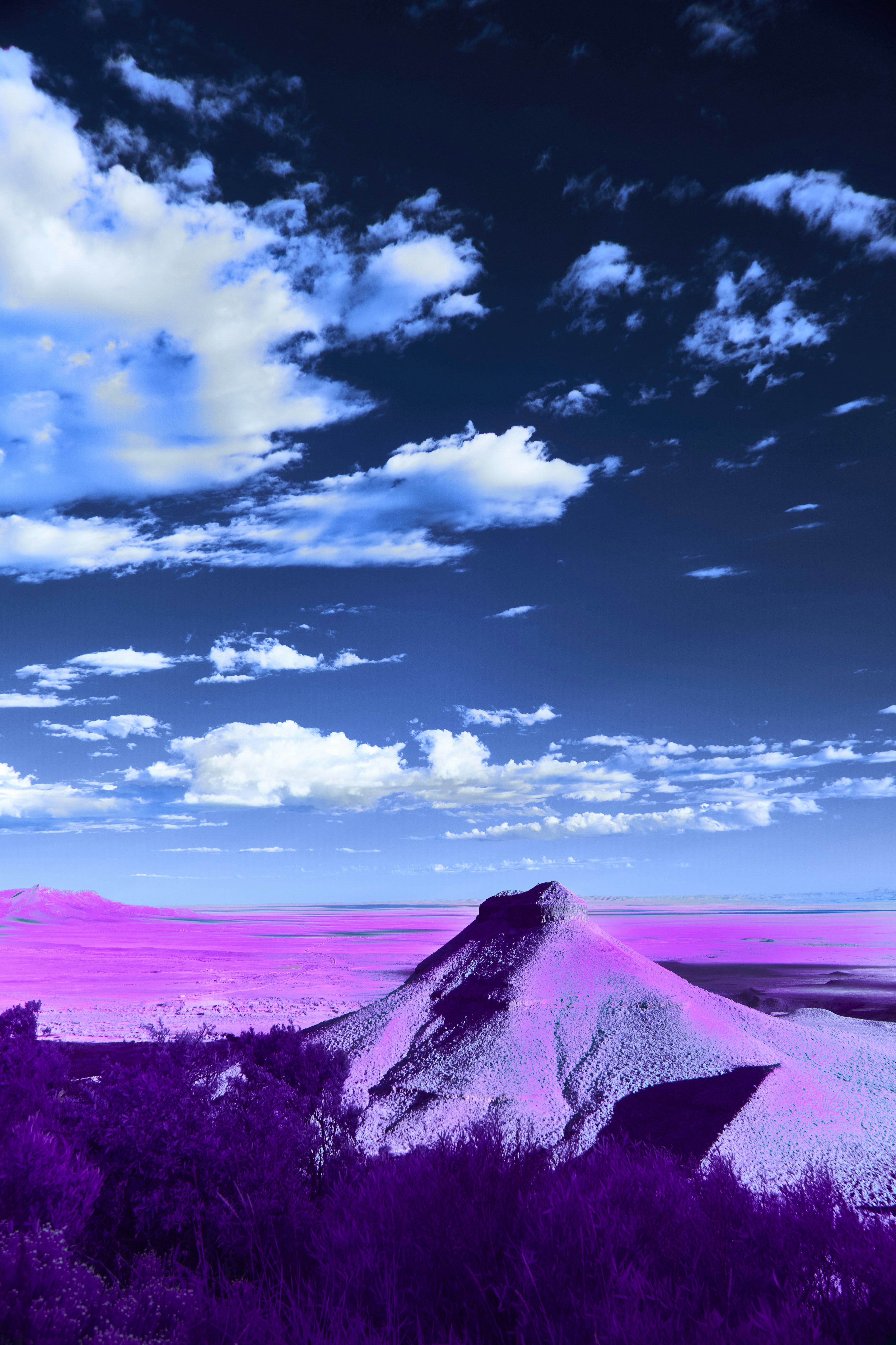 Vibrant purple mountain landscape beneath a cloudy blue sky.