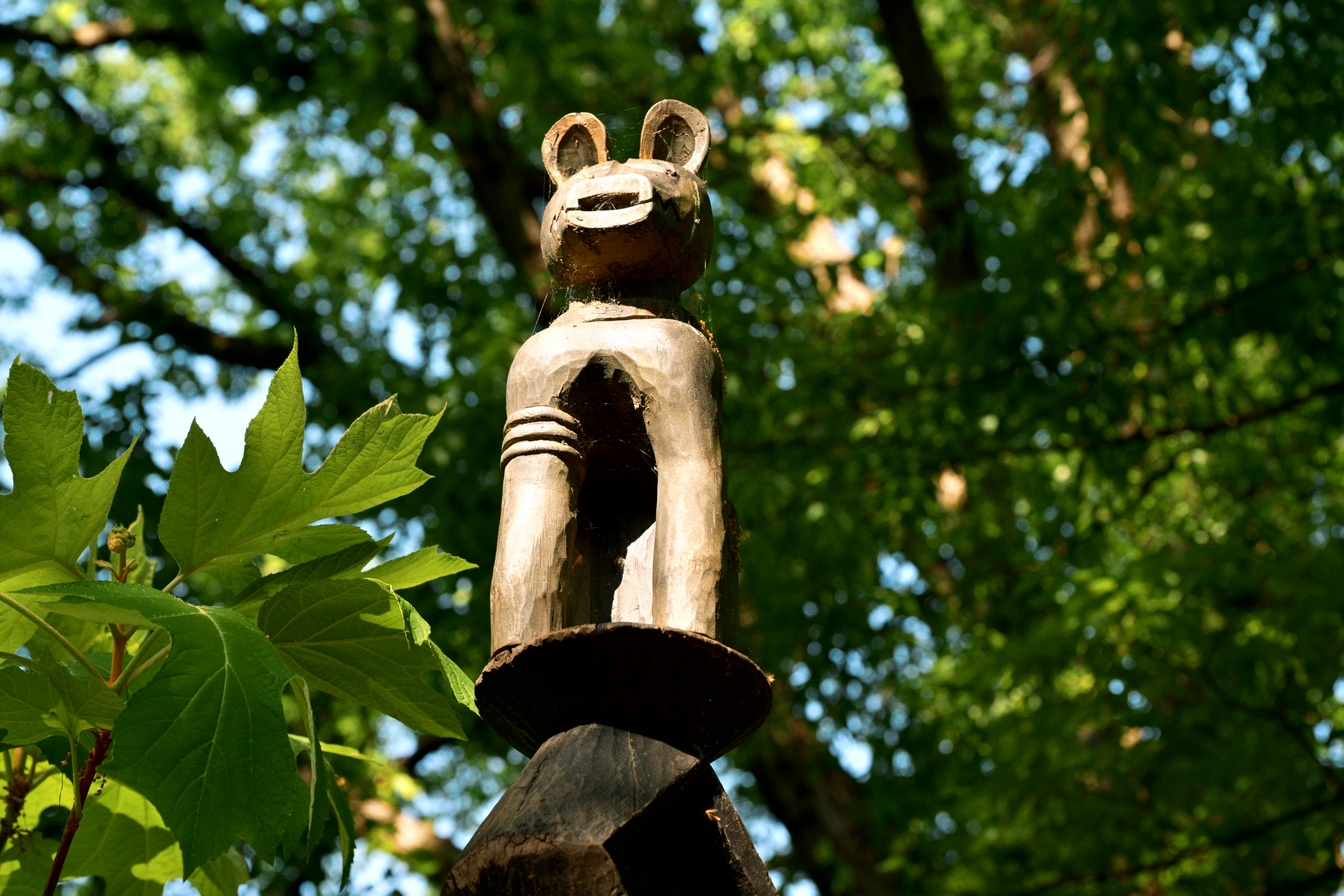 A wooden animal carving stands tall among green trees.
