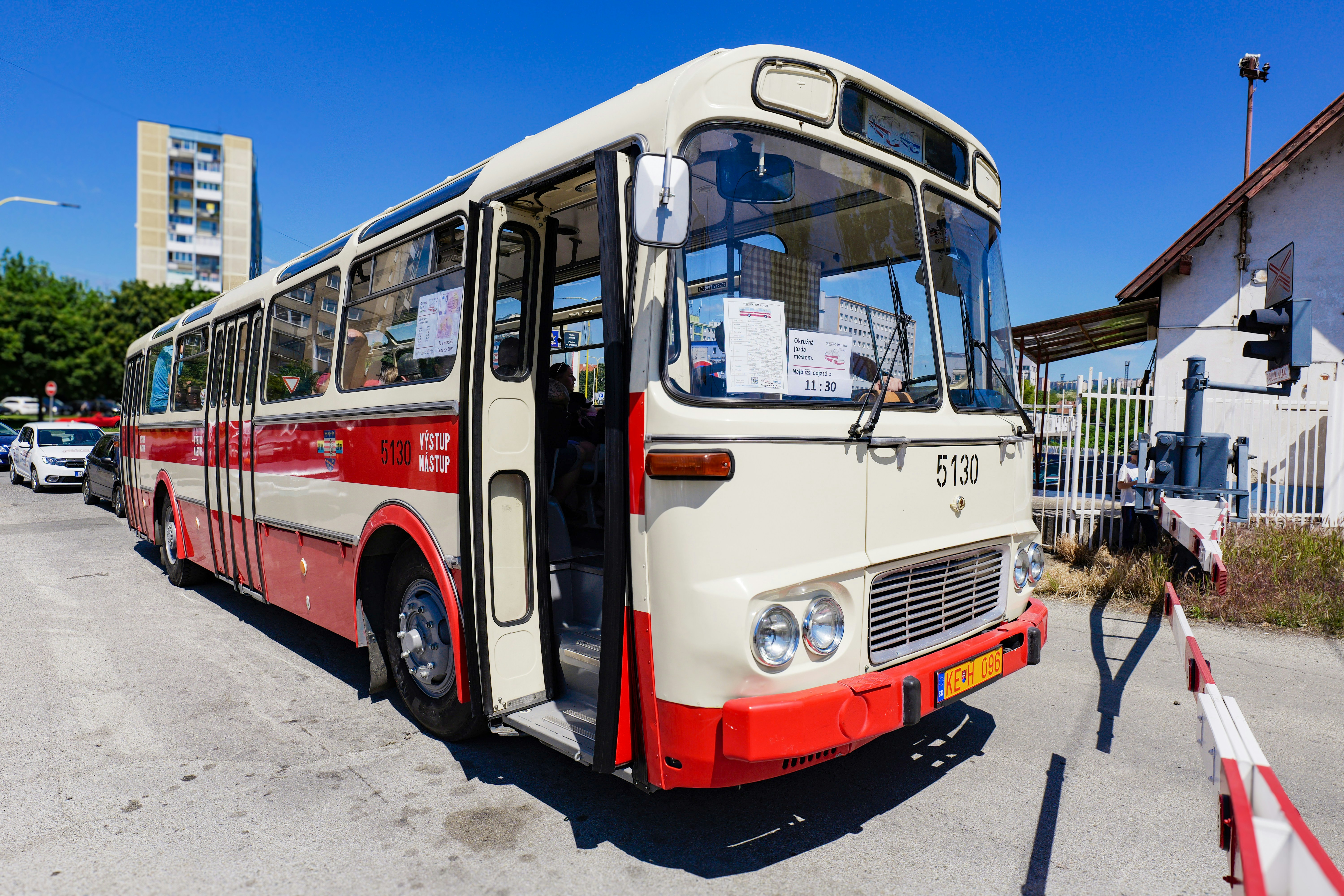 Red-and-cream bus at a station bathed in bright midday light