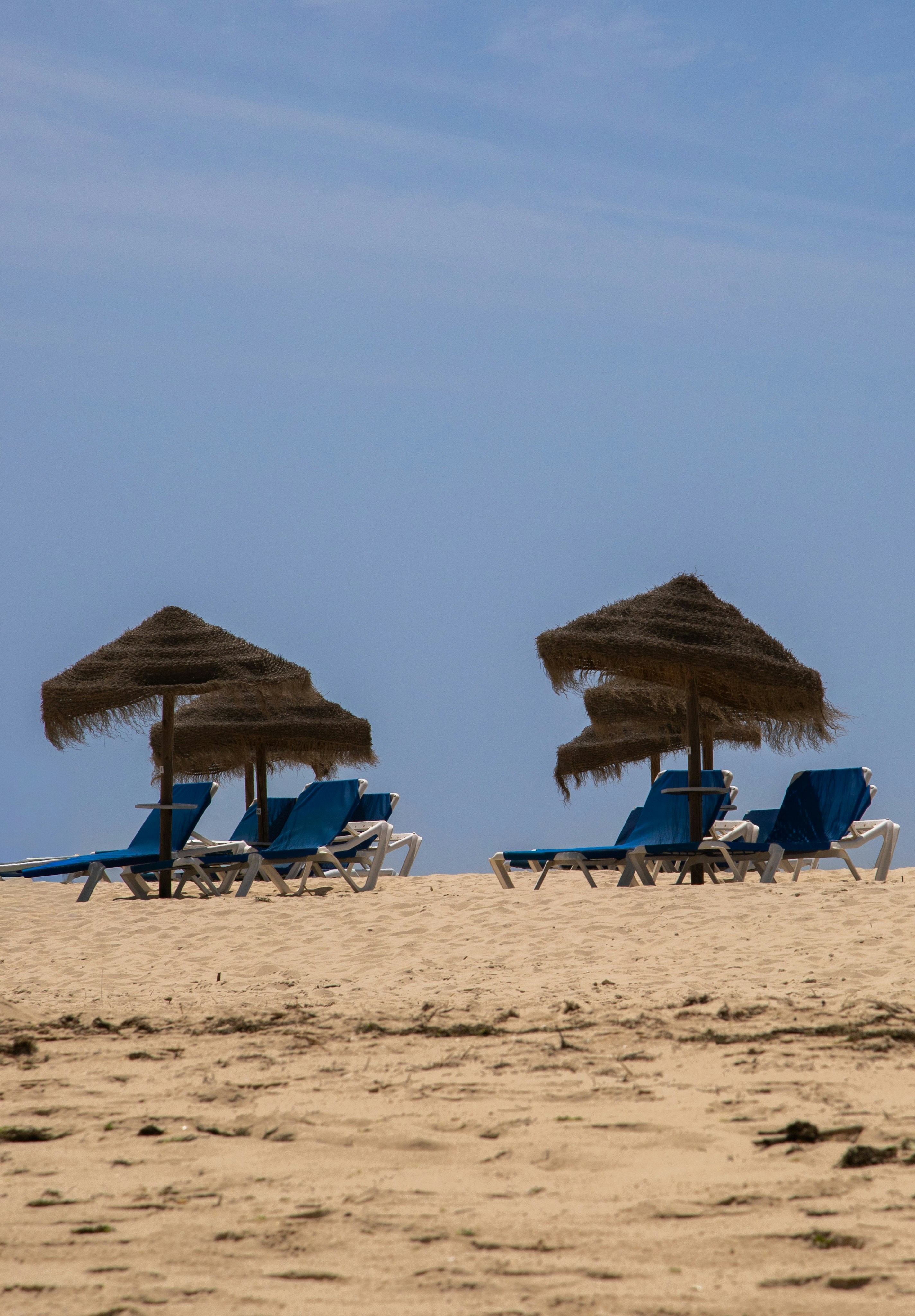 Two Stranded Oasis: Blue Lounges Under Thatched Shade on the Quiet Beach