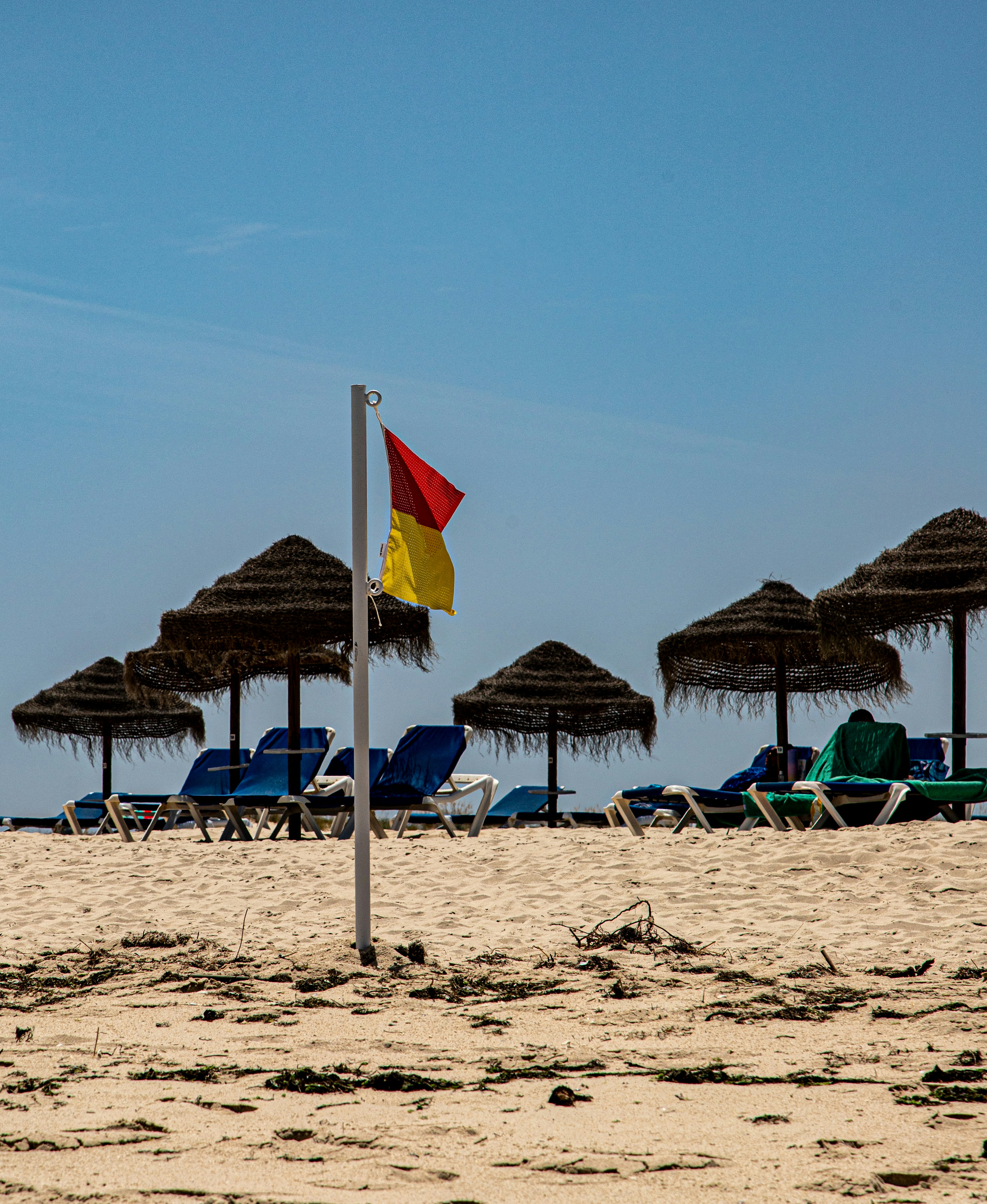 Flagpole Hue: A Quiet Beach Scene with Loungers