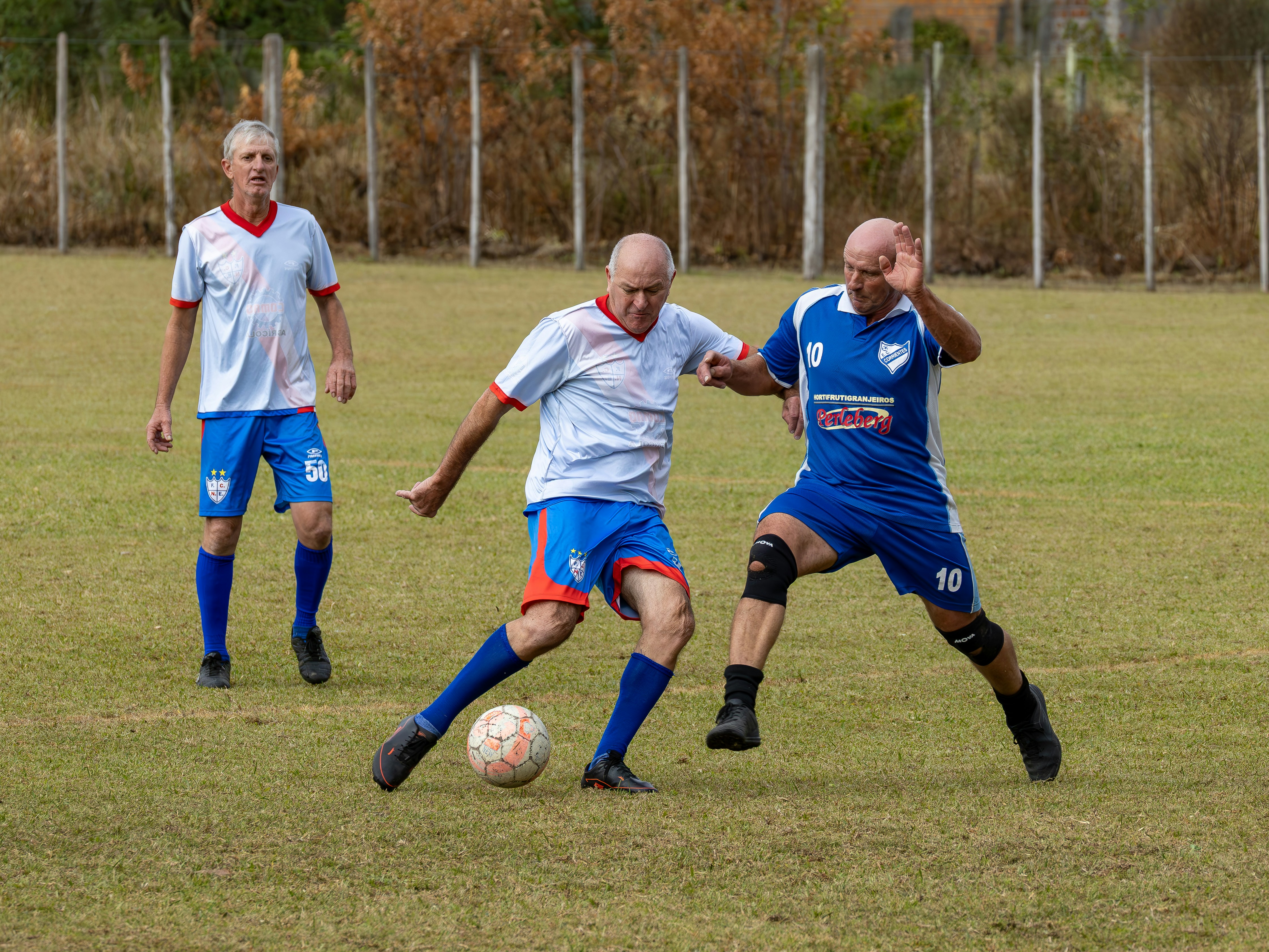 Midfield Confrontation: White-jerseyed midfielder shielded by blue-jersey rival near the ball