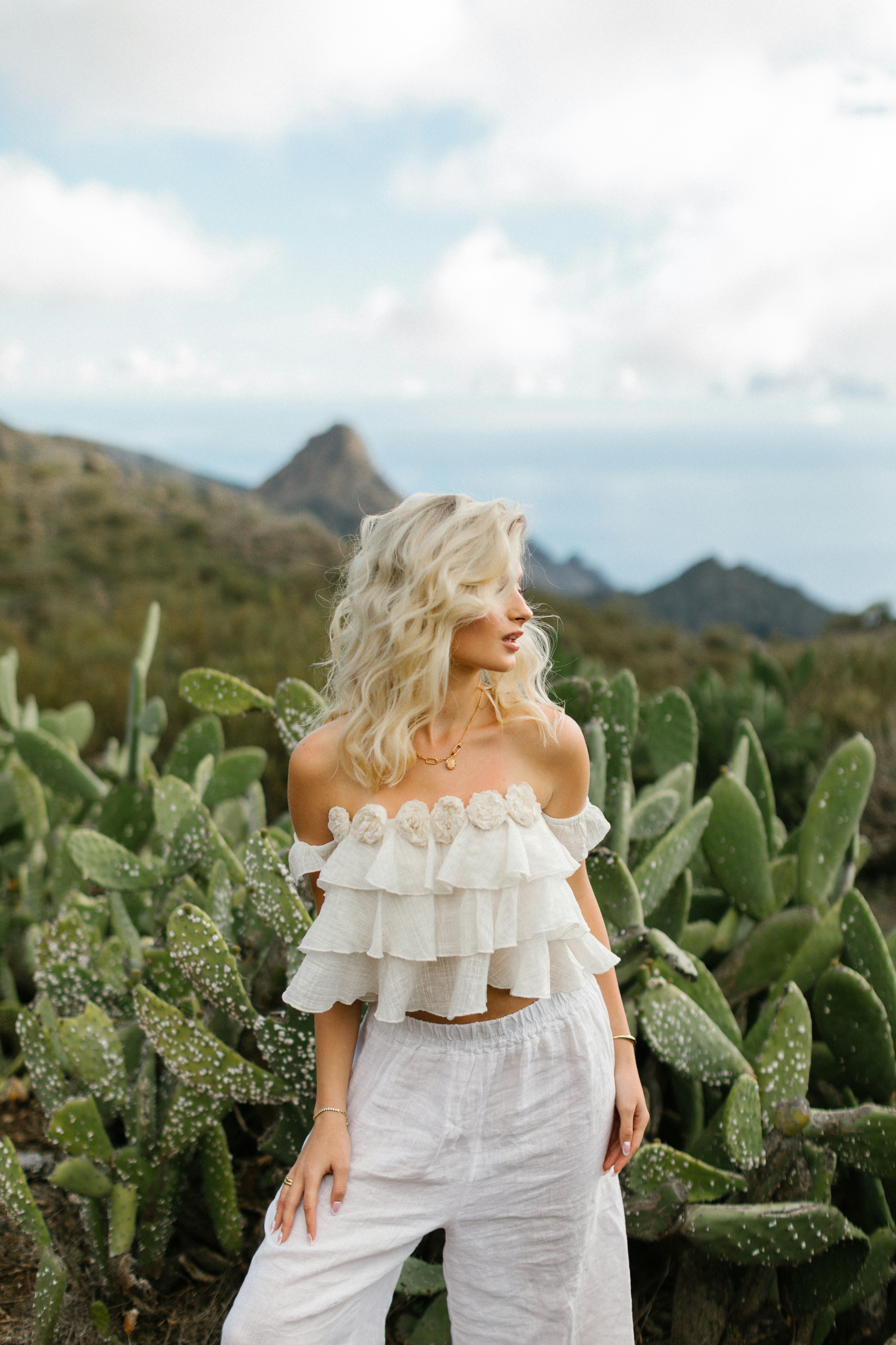 Blonde in White Ruffles Standing Among Prickly Pears by Ocean Horizon
